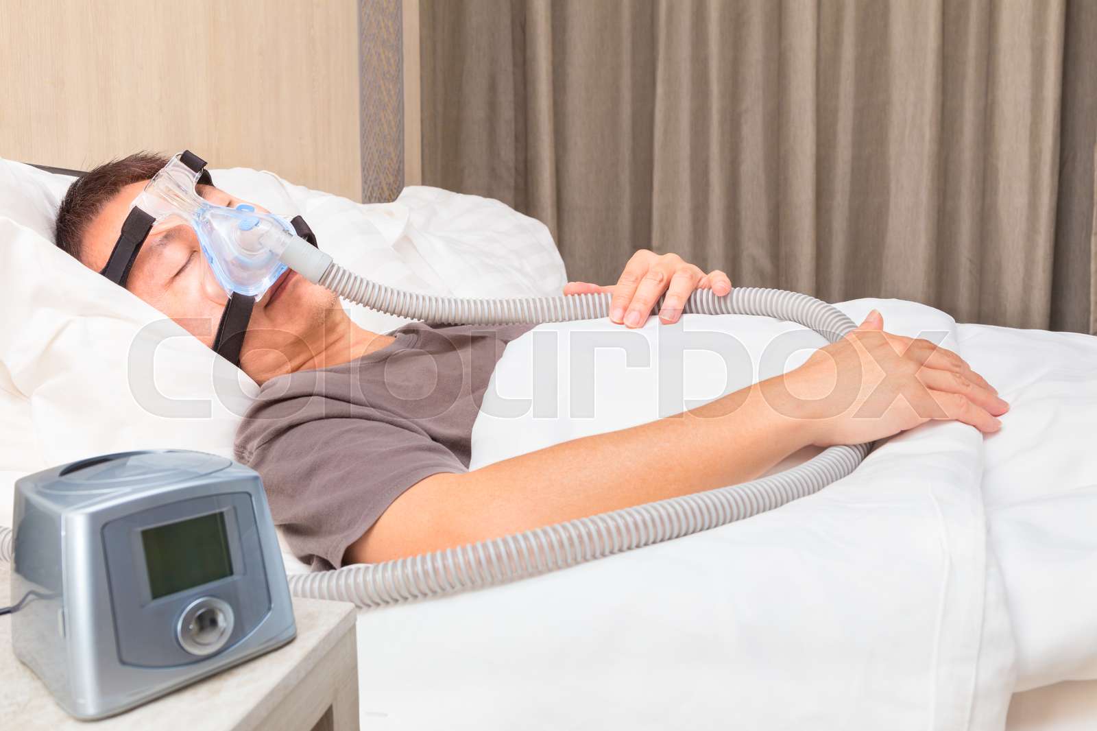 middle age asian man sleeping in bed wearing CPAP mask connecting to ...
