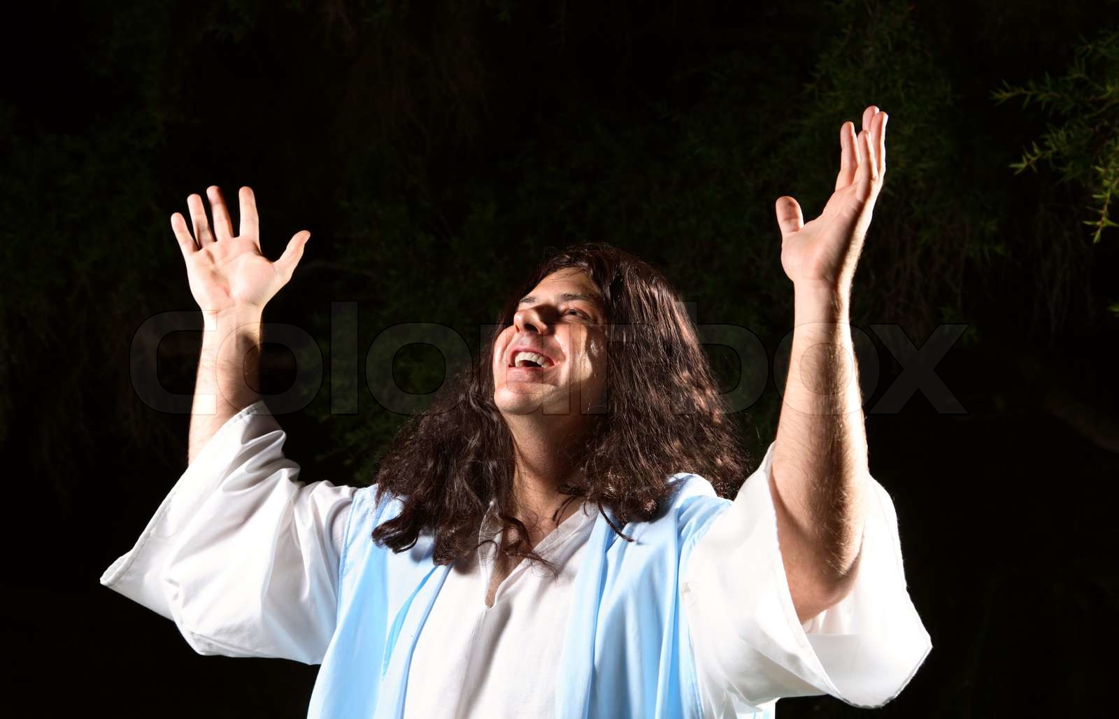 A man dressed in robe hands raised in the air praising or worshipping ...