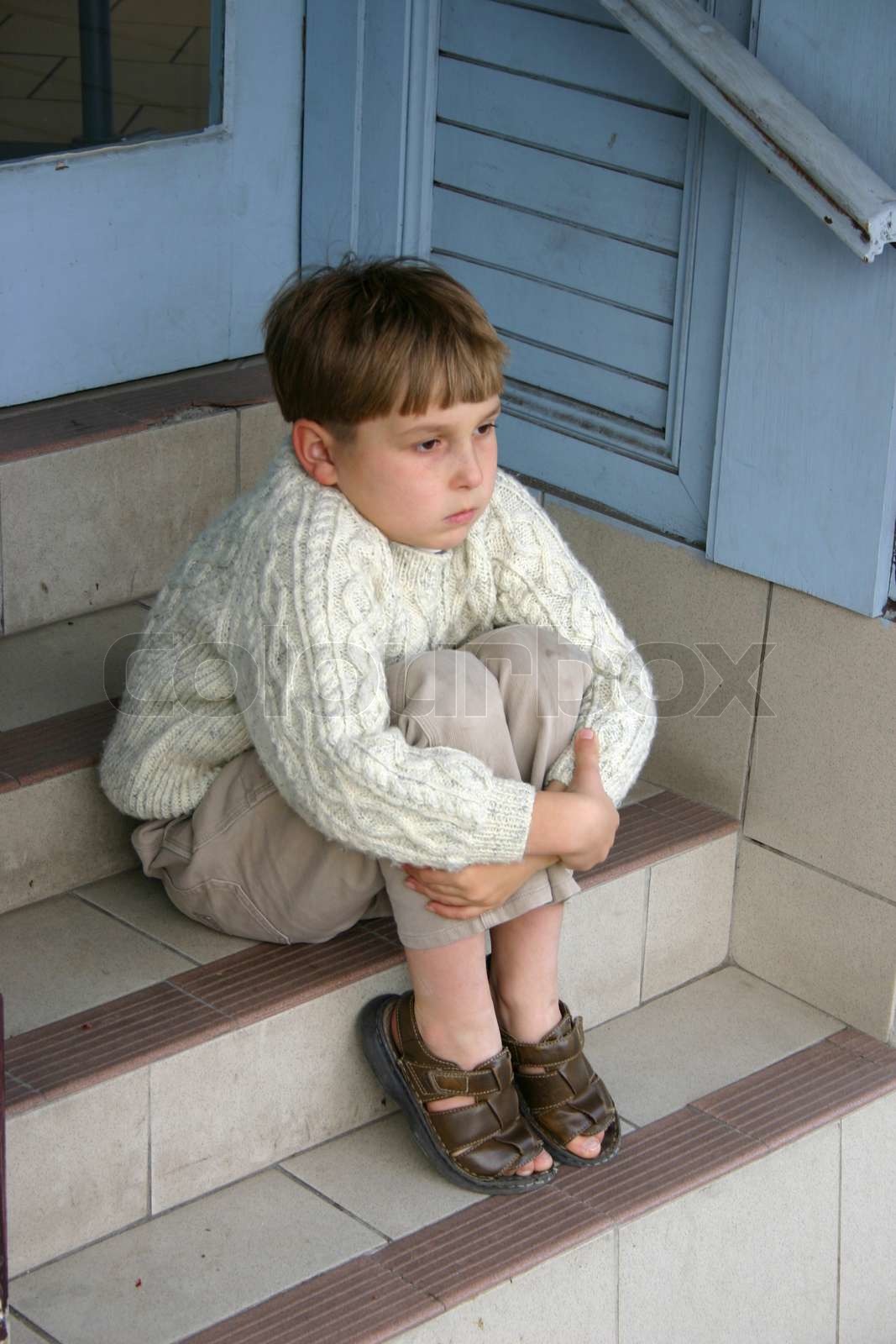 A young boy child sitting on steps of an old home | Stock image | Colourbox