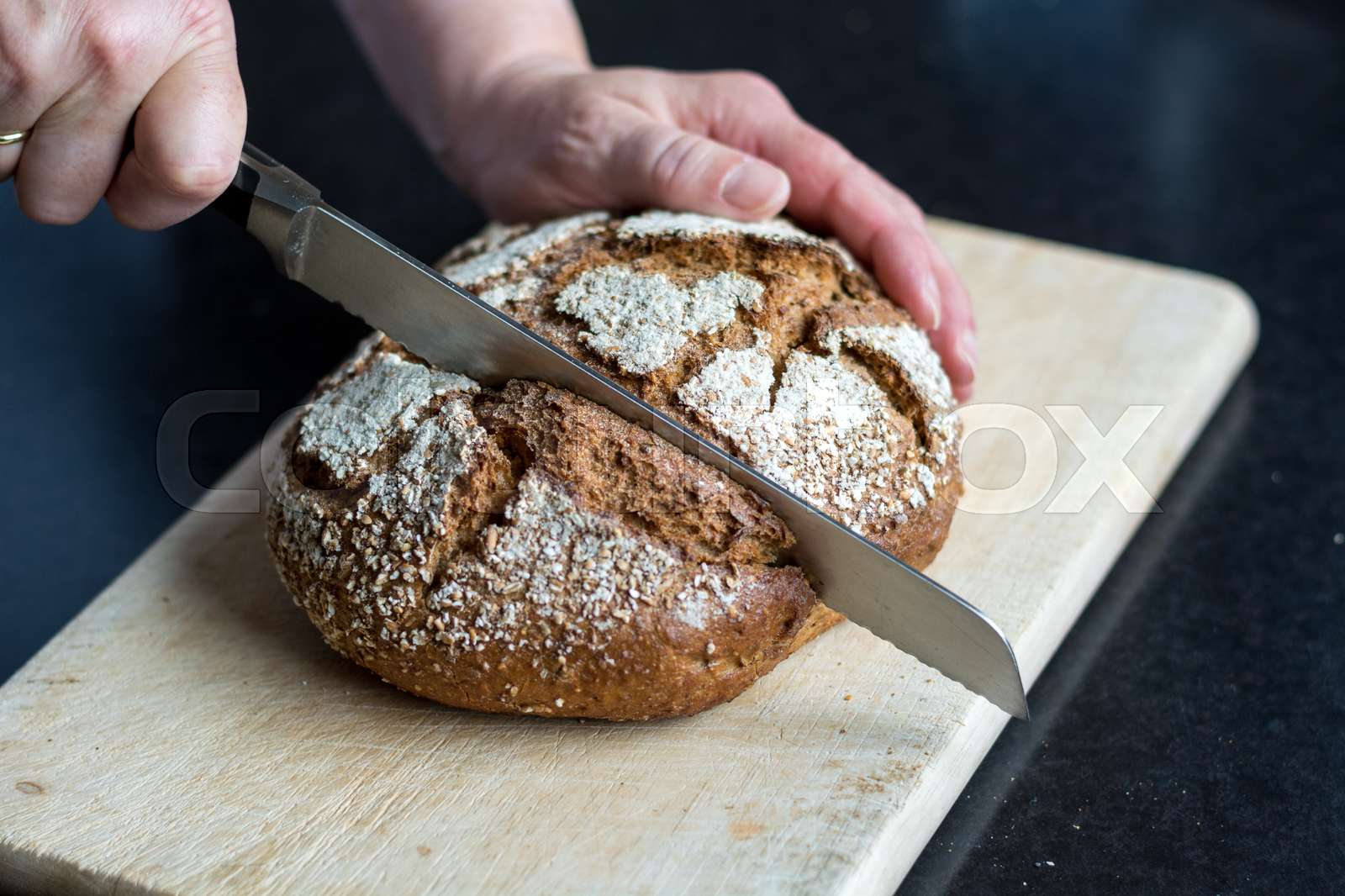 Cutting loaf of bread with knife on cutting board | Stock image | Colourbox