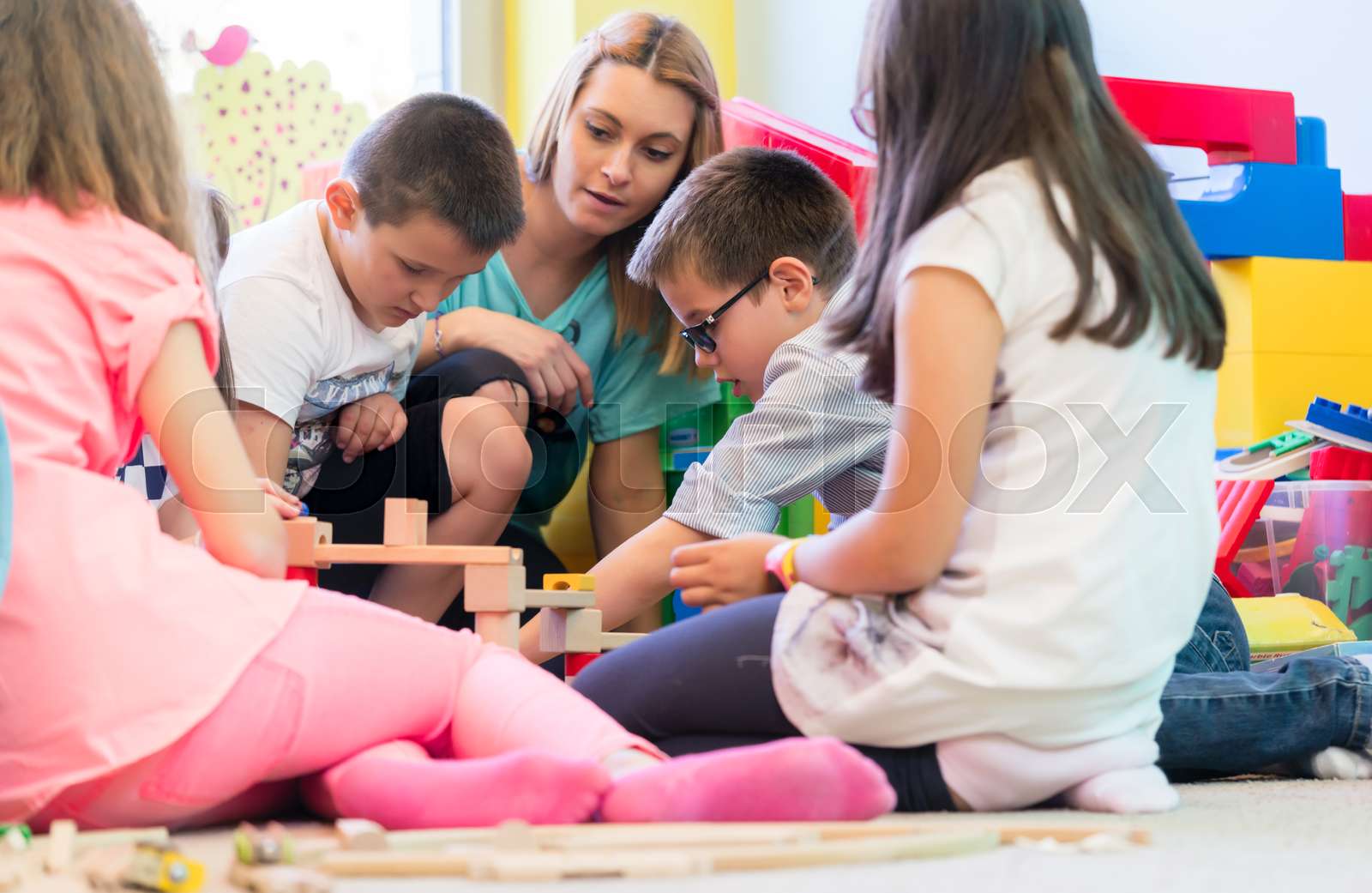 Pre-school boy cooperating with kids under guidance of kindergar ...