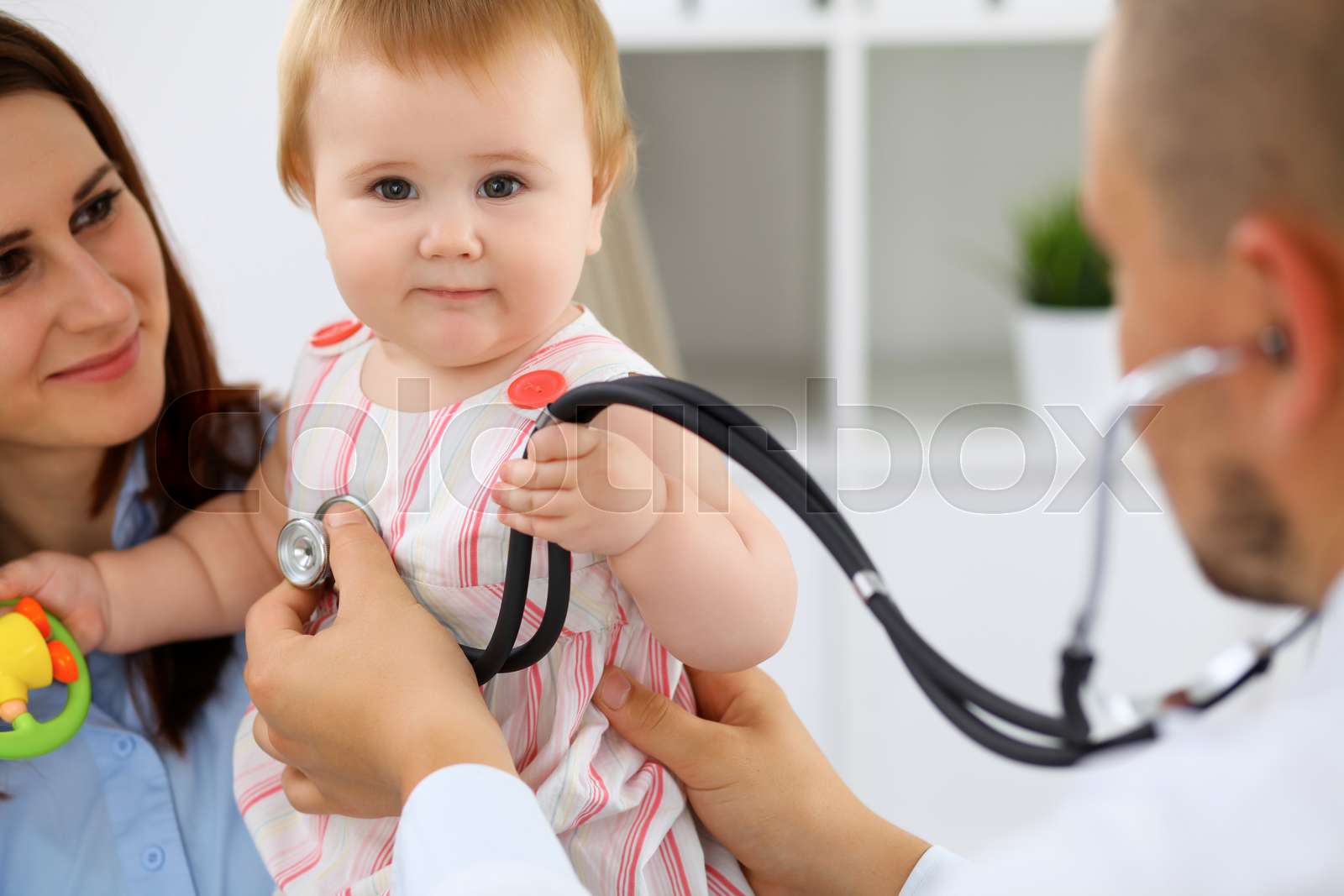 Happy cute baby with her mother at health exam at doctor's office ...