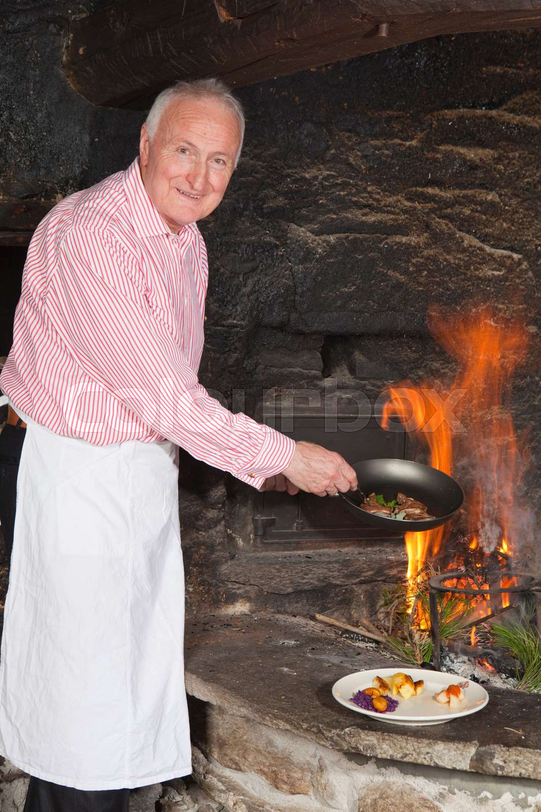 elderly cook by fireplace serving food | Stock image | Colourbox