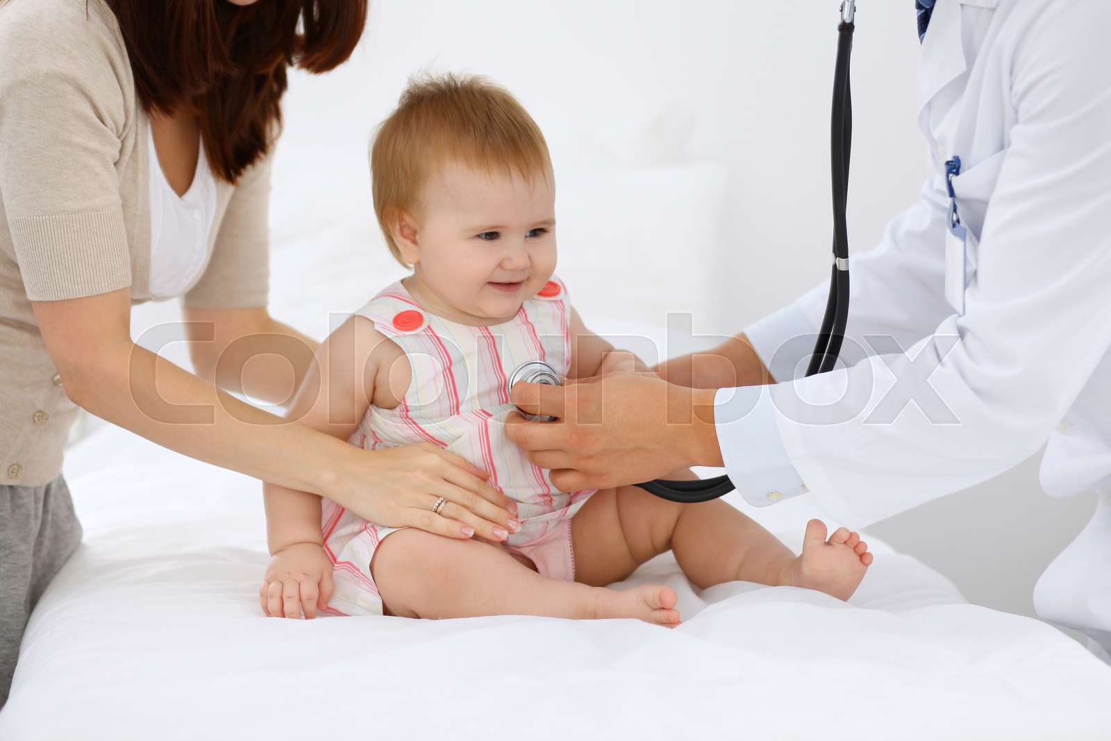 Happy cute baby with her mother at health exam at doctor's office ...