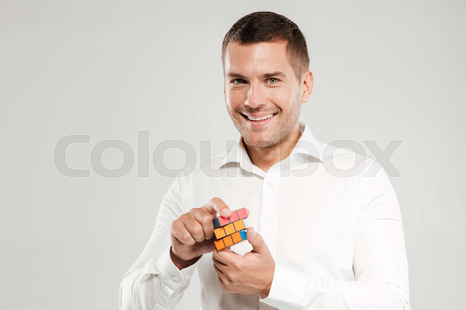 Smiling young man solve Rubik's cube. | Stock image | Colourbox