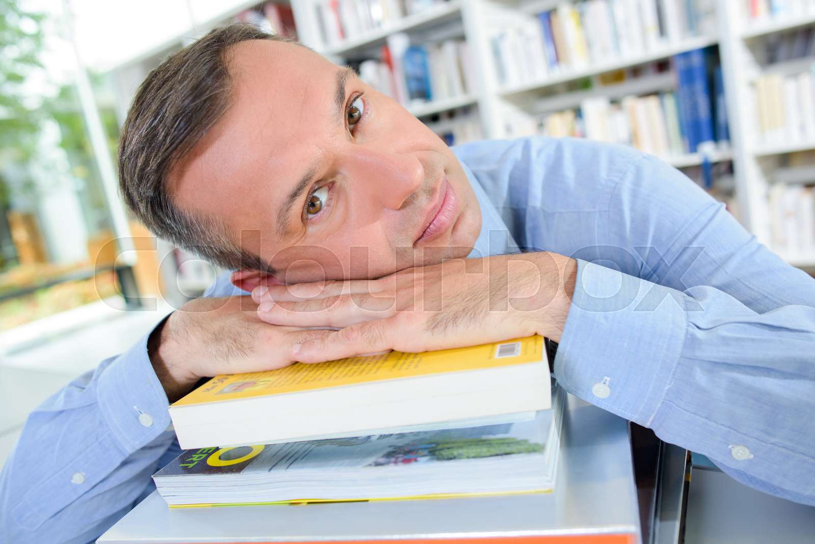 Man resting his head on stack of books | Stock image | Colourbox