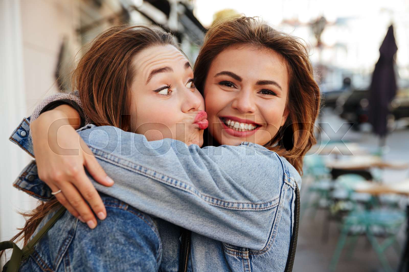 Close-up photo of two happy pretty woman friends in jeans jacket hugging each other on city ...
