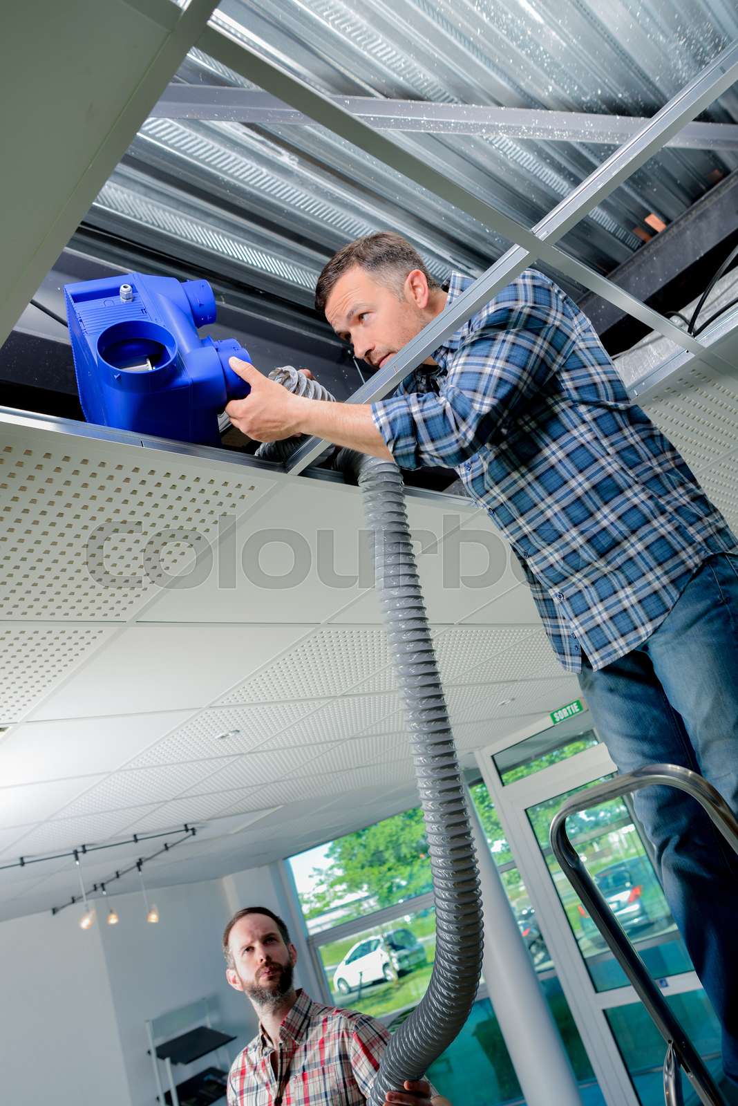 Builder fitting flexible hose in roof space | Stock image | Colourbox
