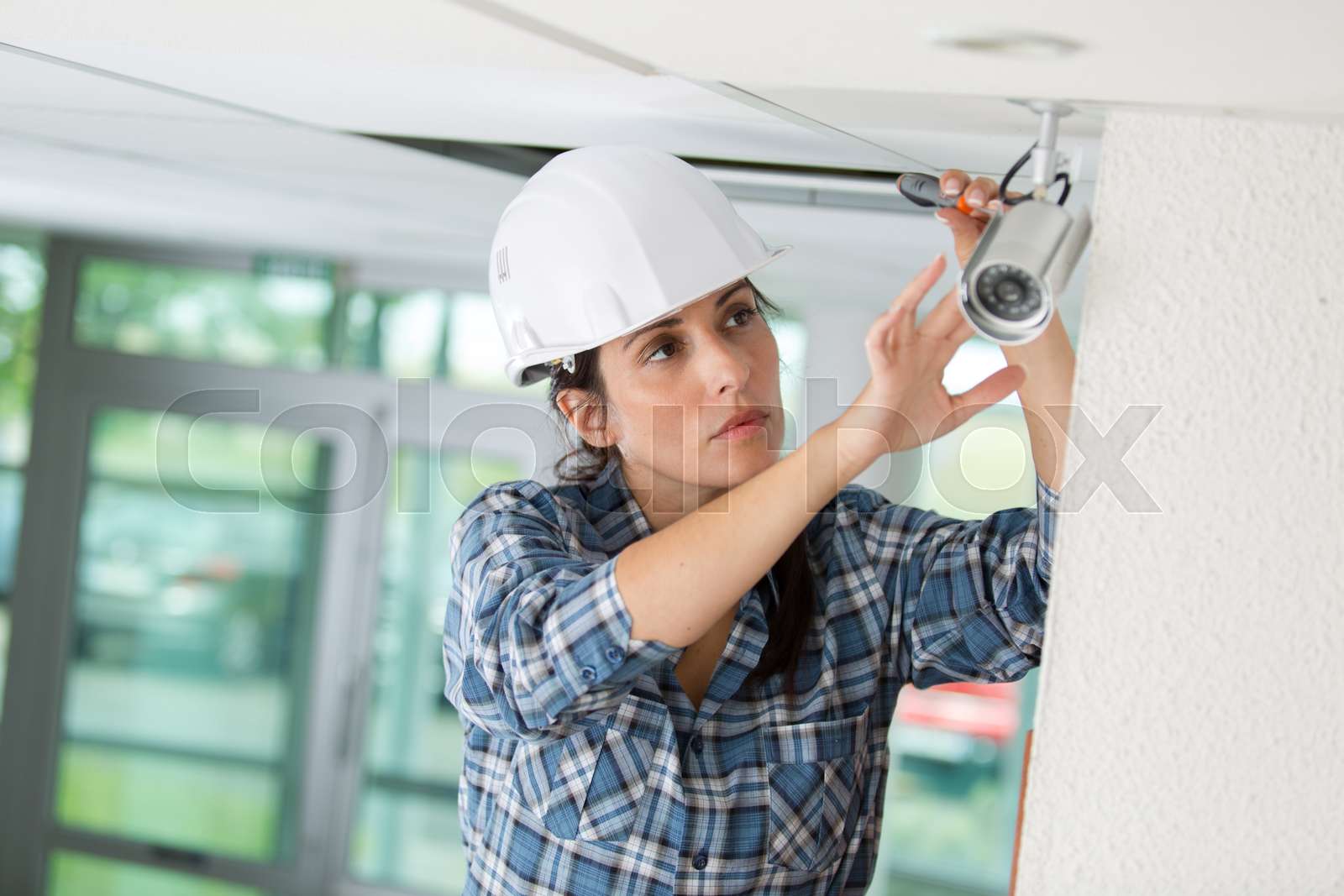 female cctv installer hinstalling security camera | Stock image | Colourbox