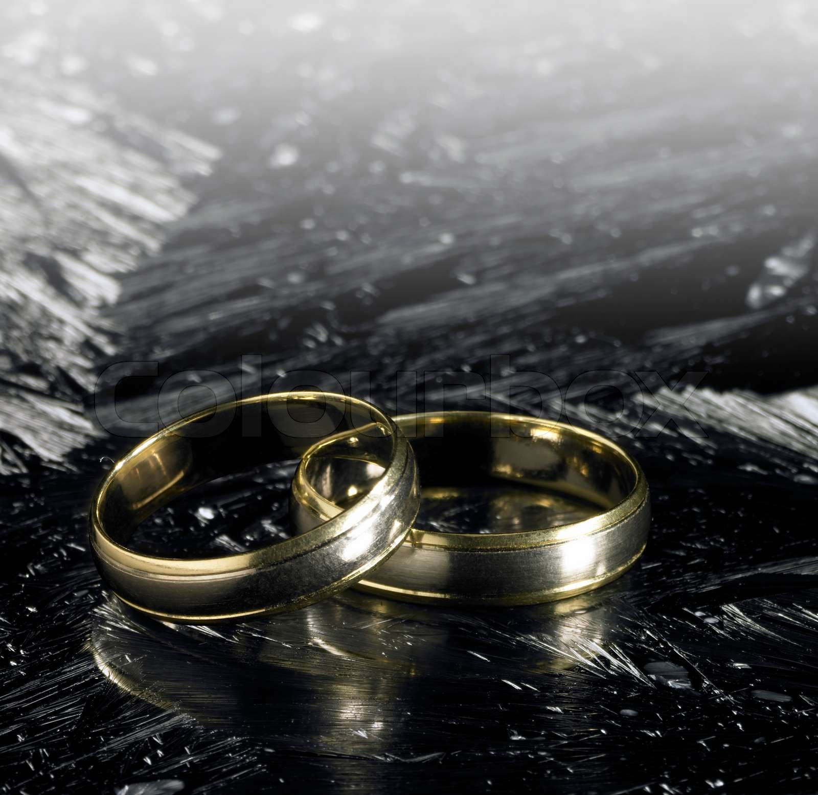 studio photography of two golden wedding rings on each other in icy ...
