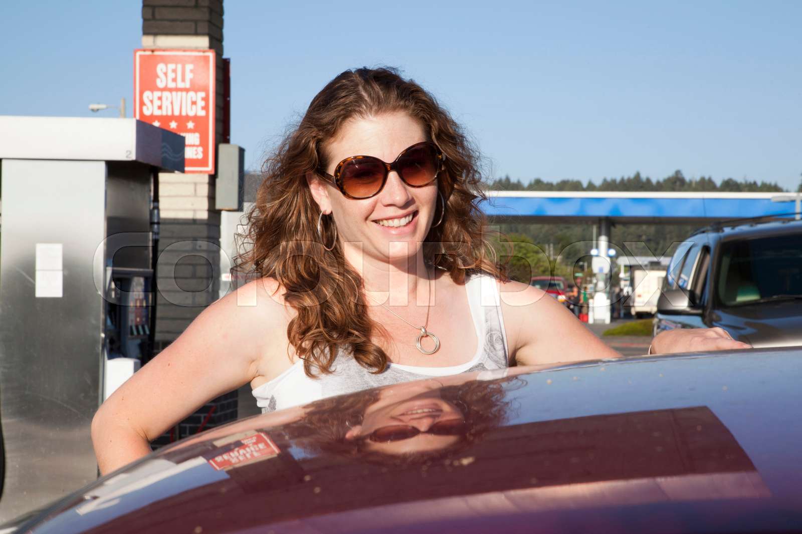 Smiling woman pumping gas at station | Stock image | Colourbox
