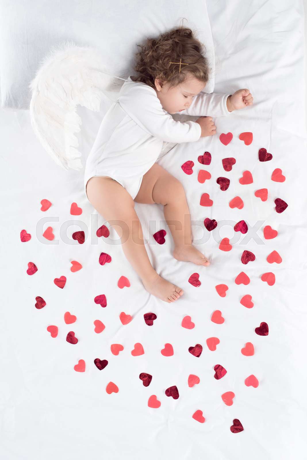 cupid with wings sleeping on bed with red hearts | Stock image | Colourbox