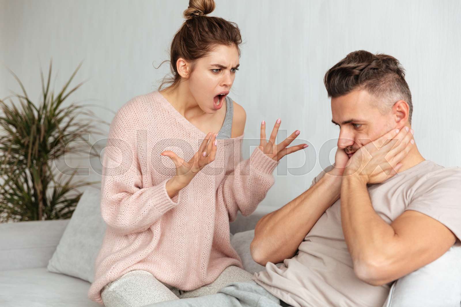 Confused man sitting on couch with him girlfriend which screaming ...