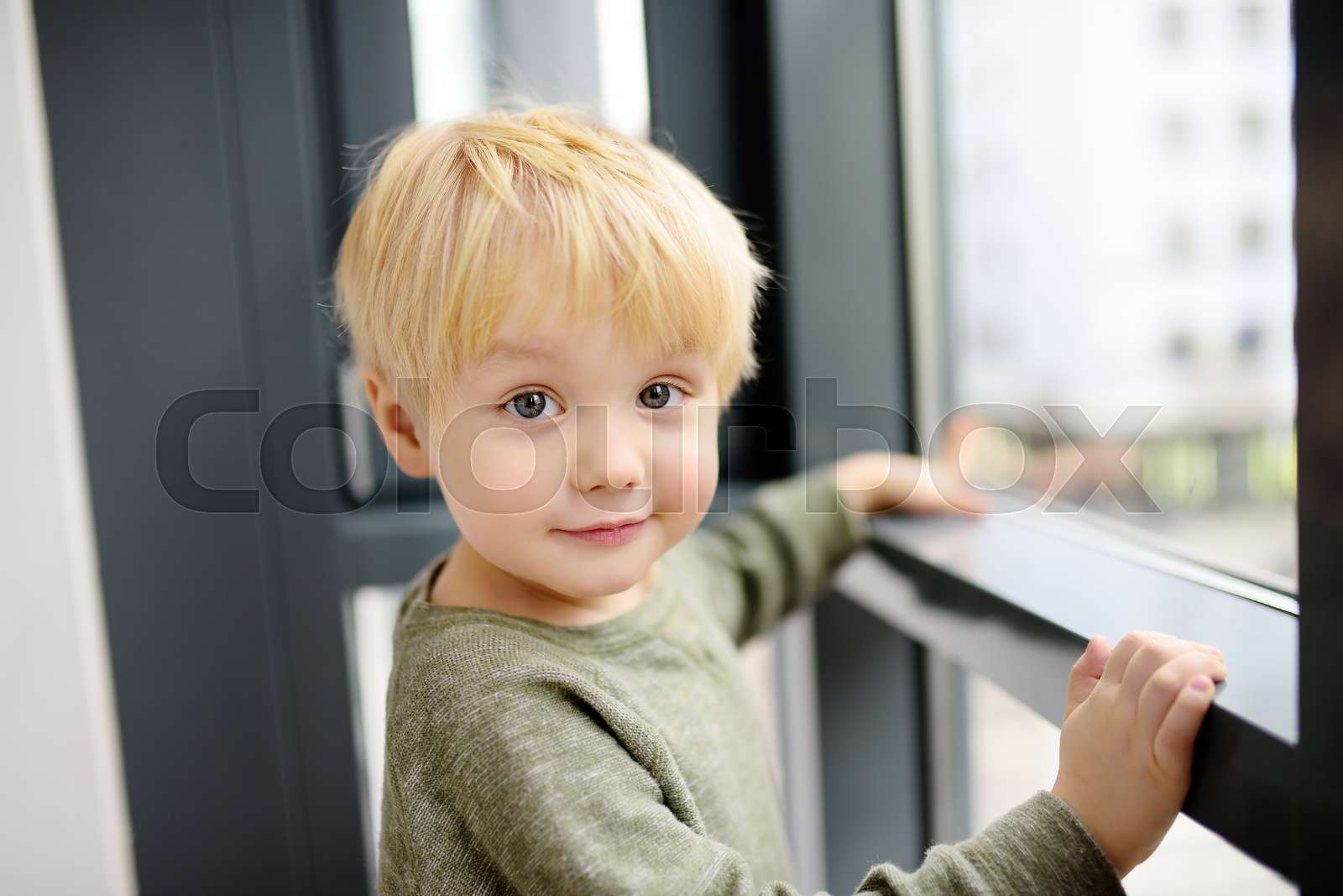 Lovely little boy sitting on the window near panoramic window and ...