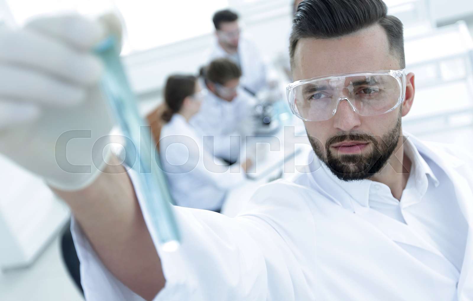 image is blurred. young scientist holding tube with the reagents ...