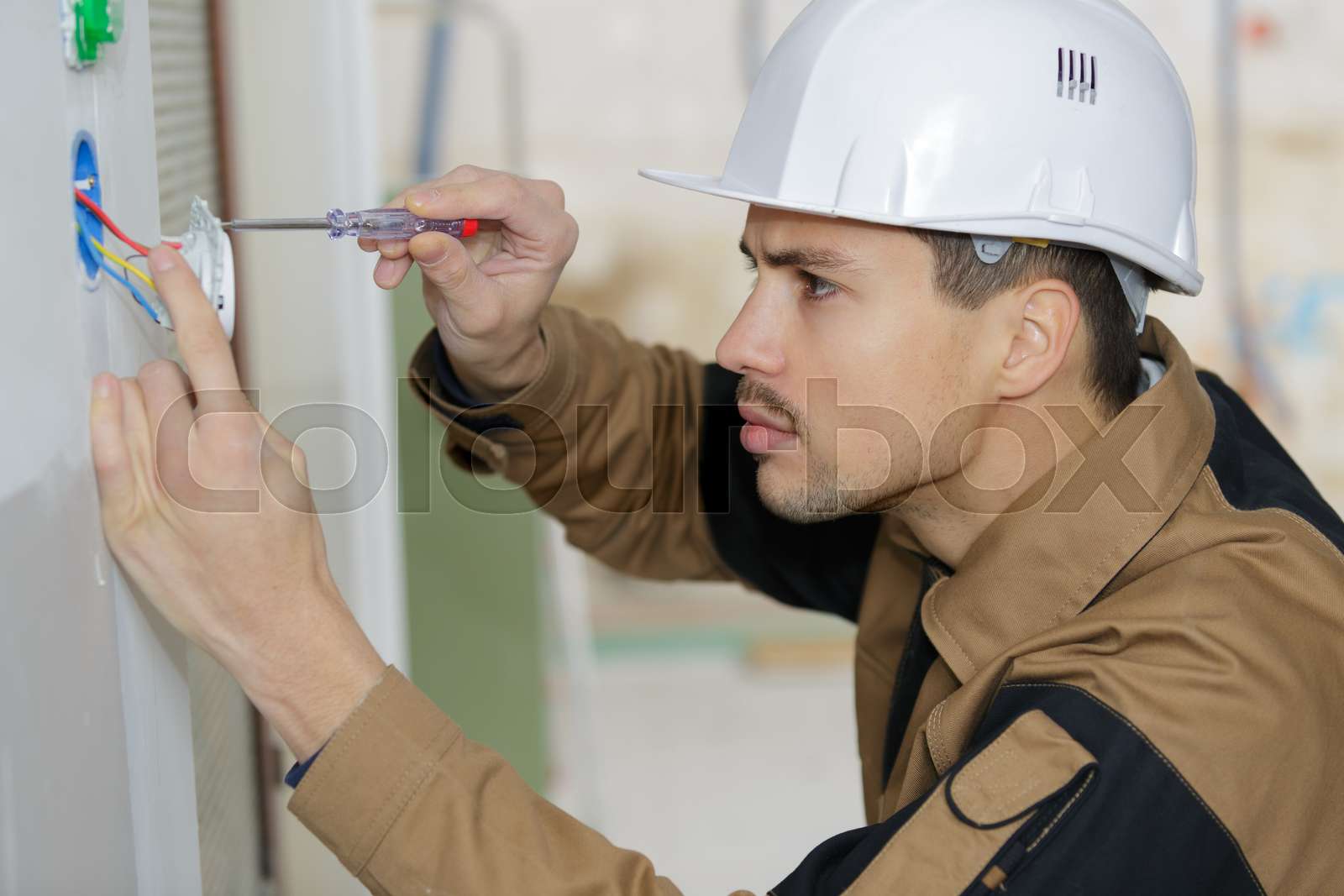 young electrician installing electrical socket on wall with screwdriver ...