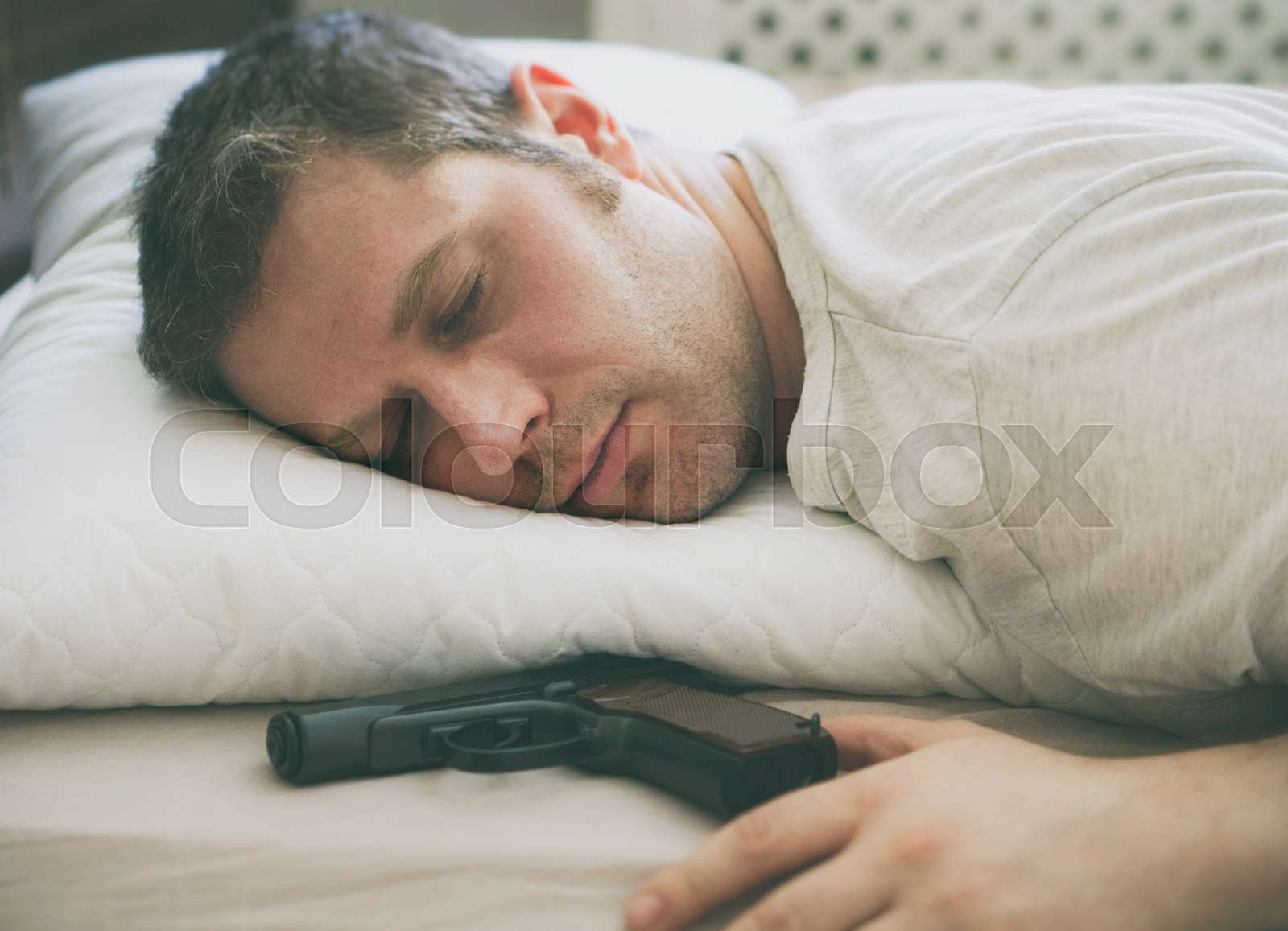 Man sleeping in bed with gun near his hand. | Stock image | Colourbox