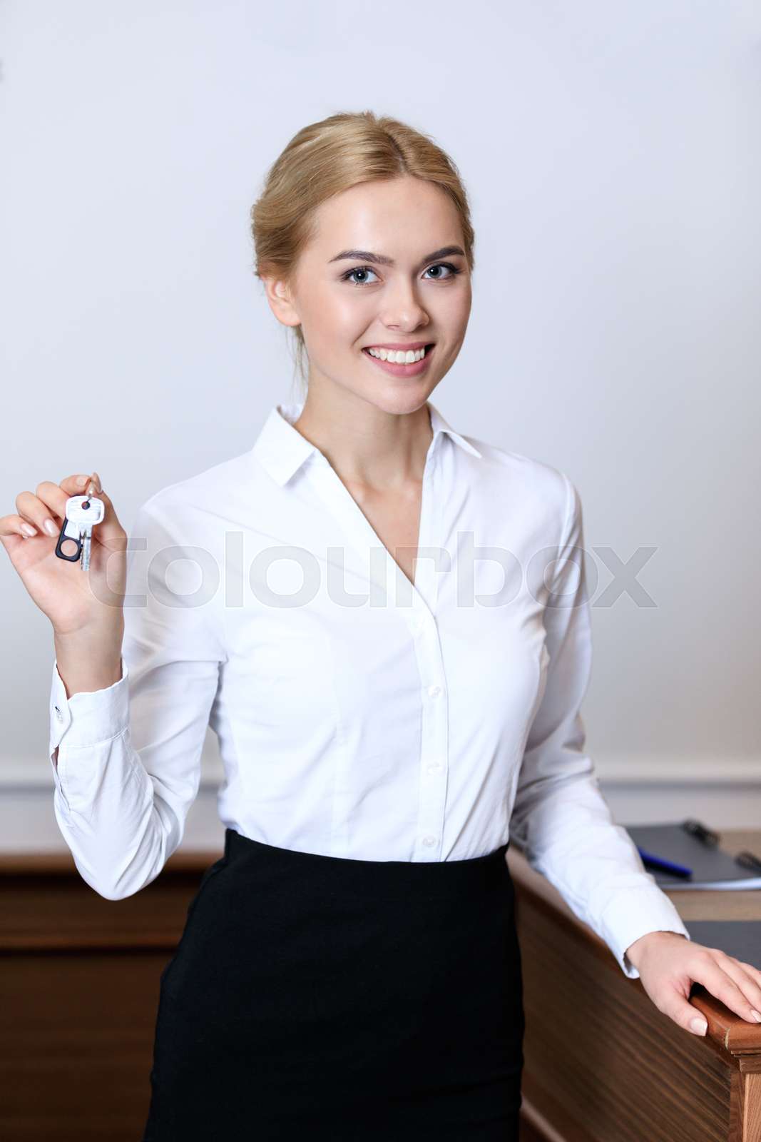 smiling attractive receptionist holding key at reception desk | Stock ...