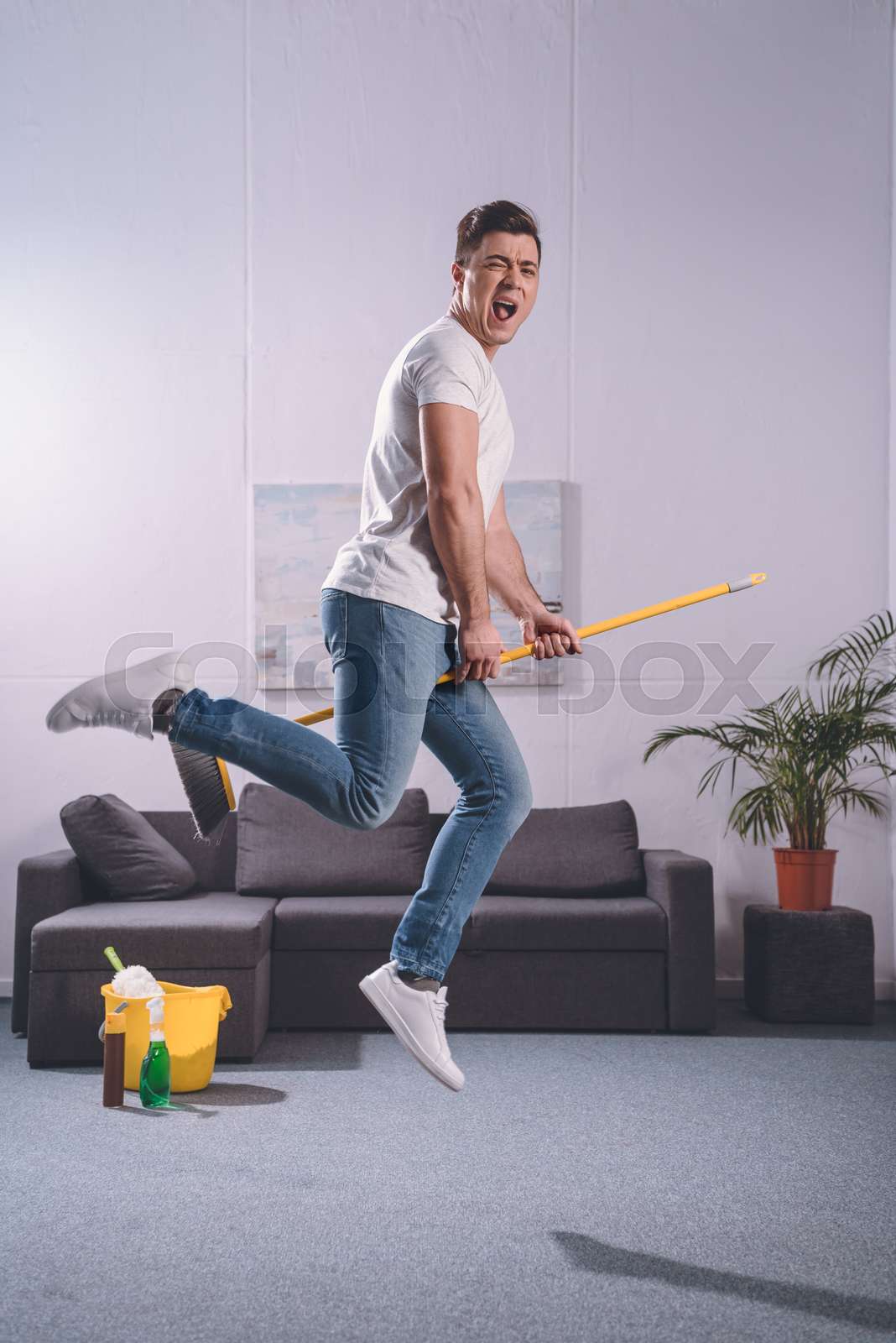 handsome man jumping with broom in living room | Stock image | Colourbox