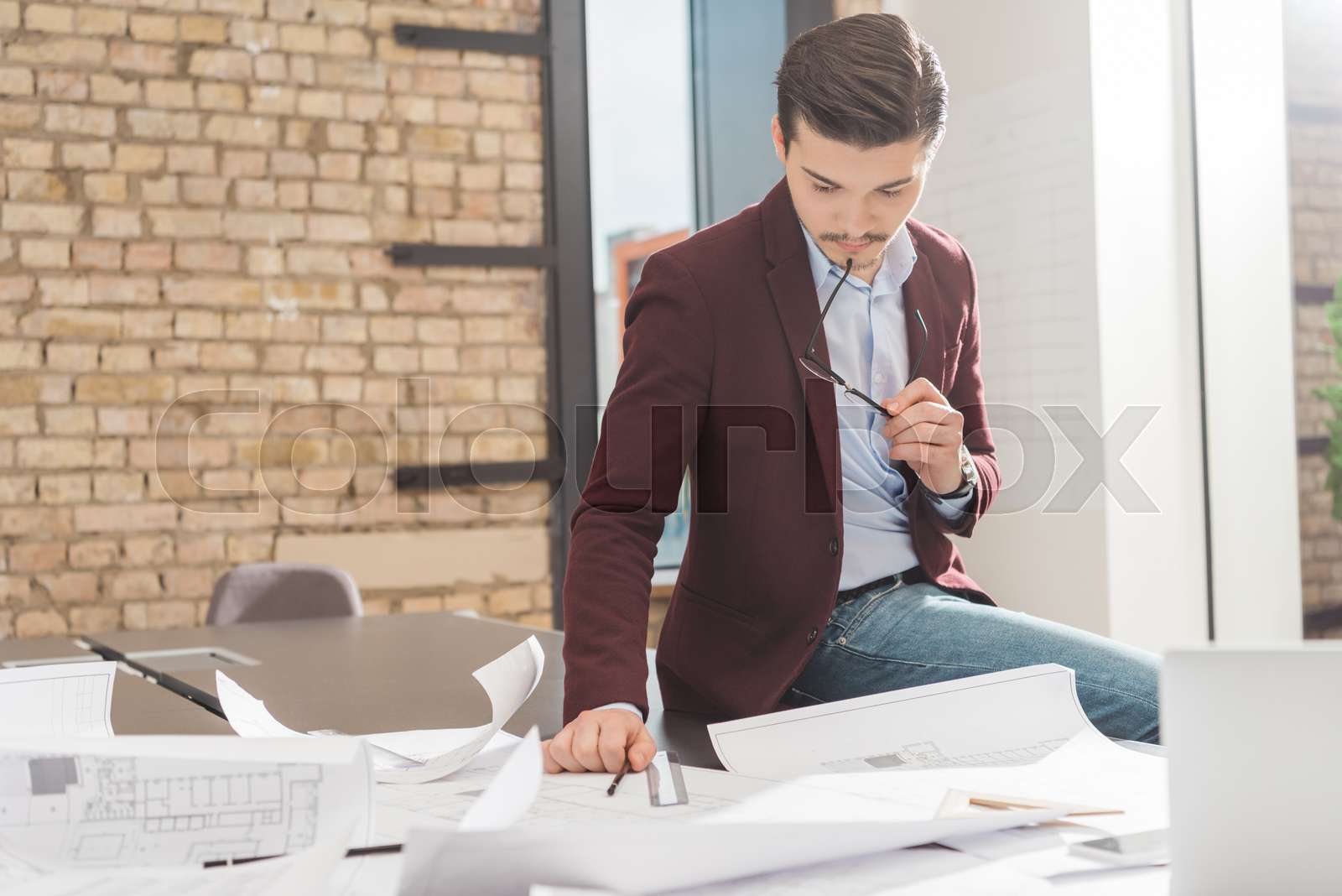 thoughtful young architect sitting on work table with building plans at ...