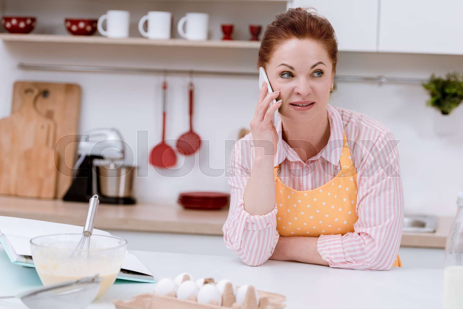 beautiful mature woman talking by phone while cooking at kitchen ...
