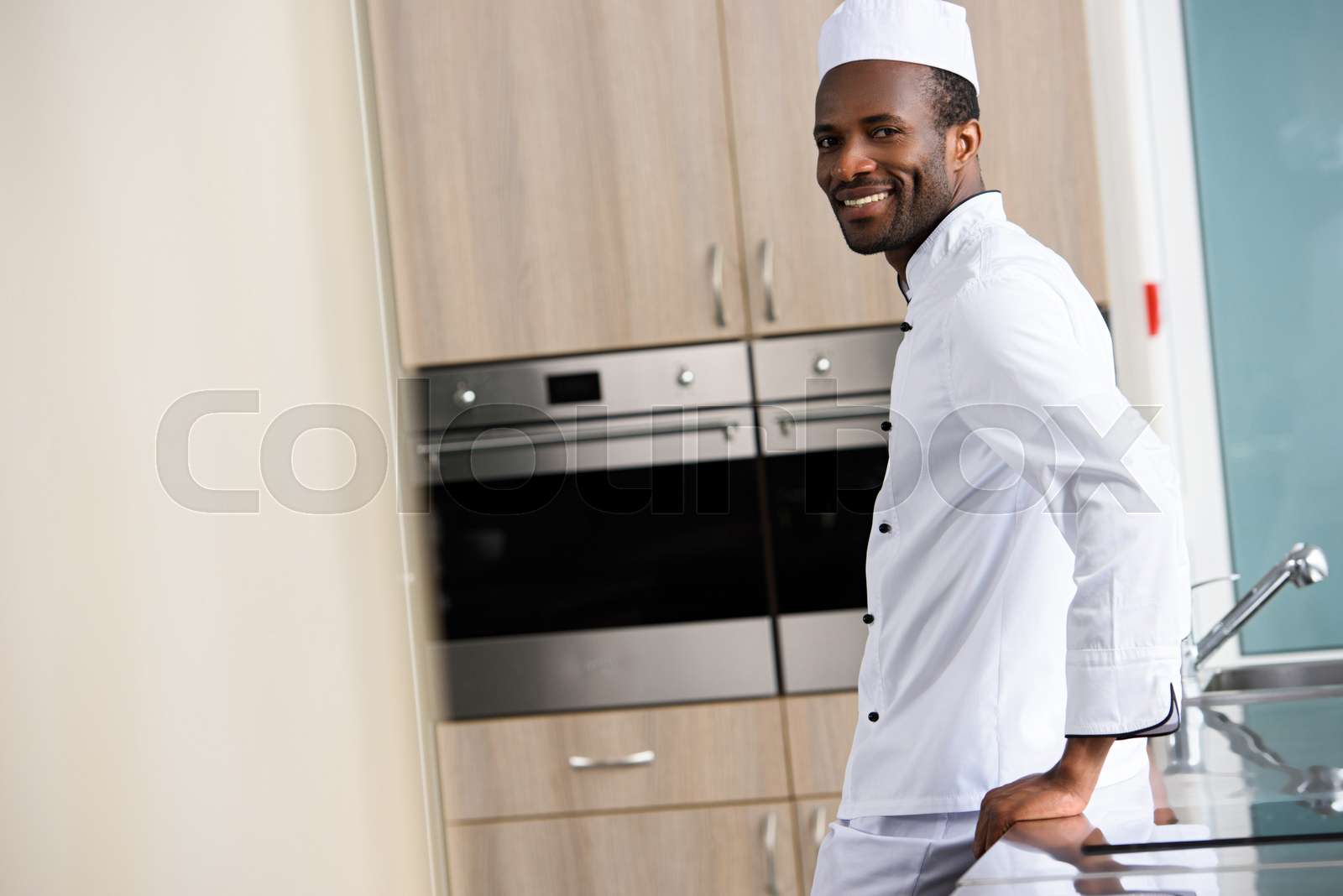 side view of handsome african american chef leaning on kitchen counter ...