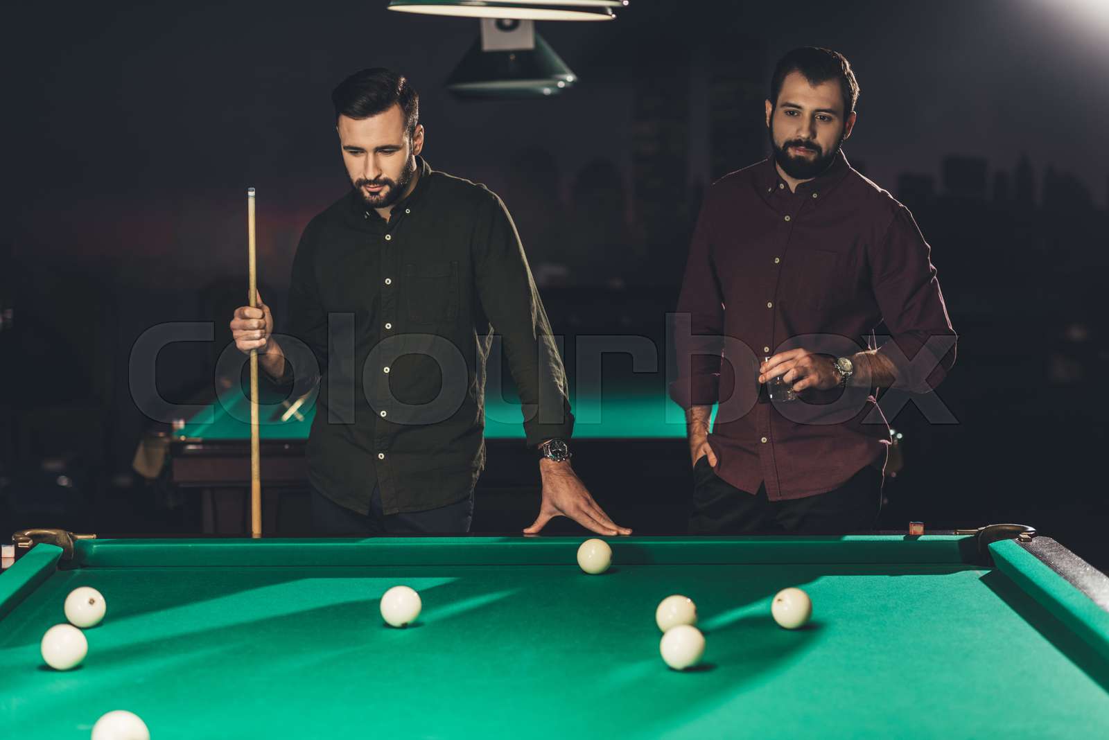 couple of successful men standing beside pool table with drink at bar ...