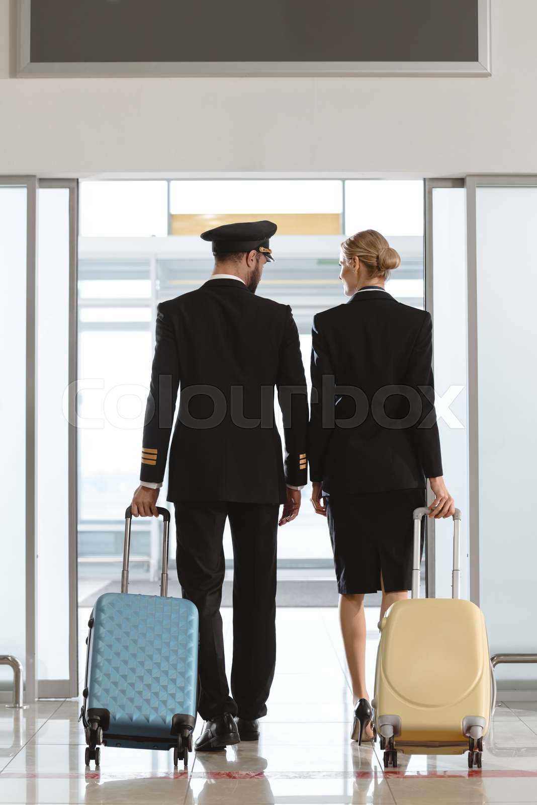 rear view of pilot and stewardess walking by departure area | Stock ...