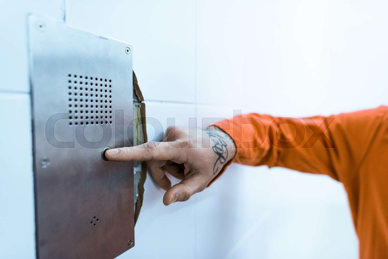cropped image of tattooed prisoner in orange uniform pressing button in ...