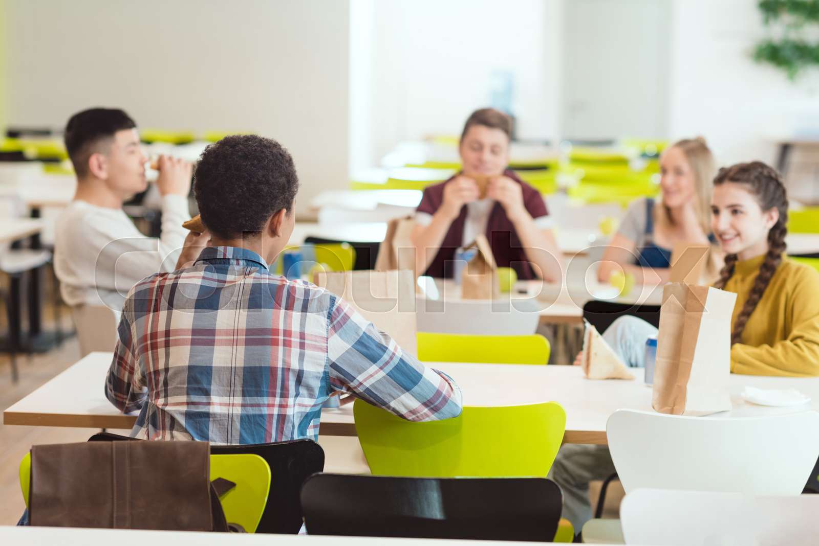 group of teenage students chatting while taking lunch at school ...