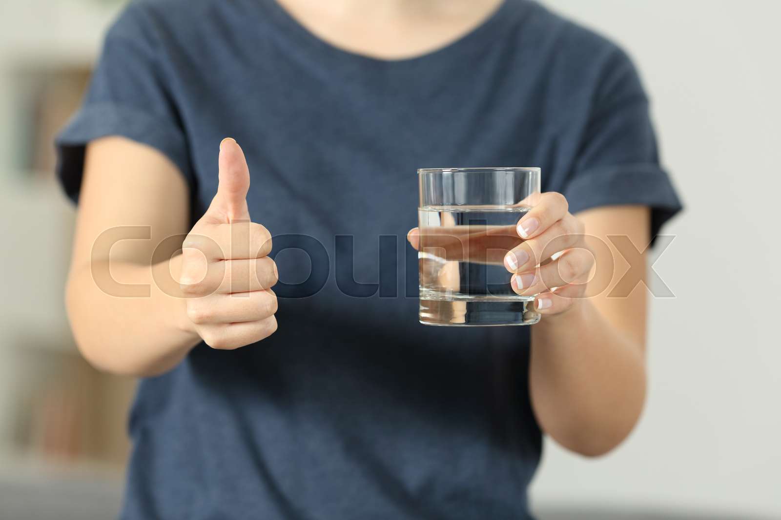 Woman holding a water glass with thumbs up | Stock image | Colourbox