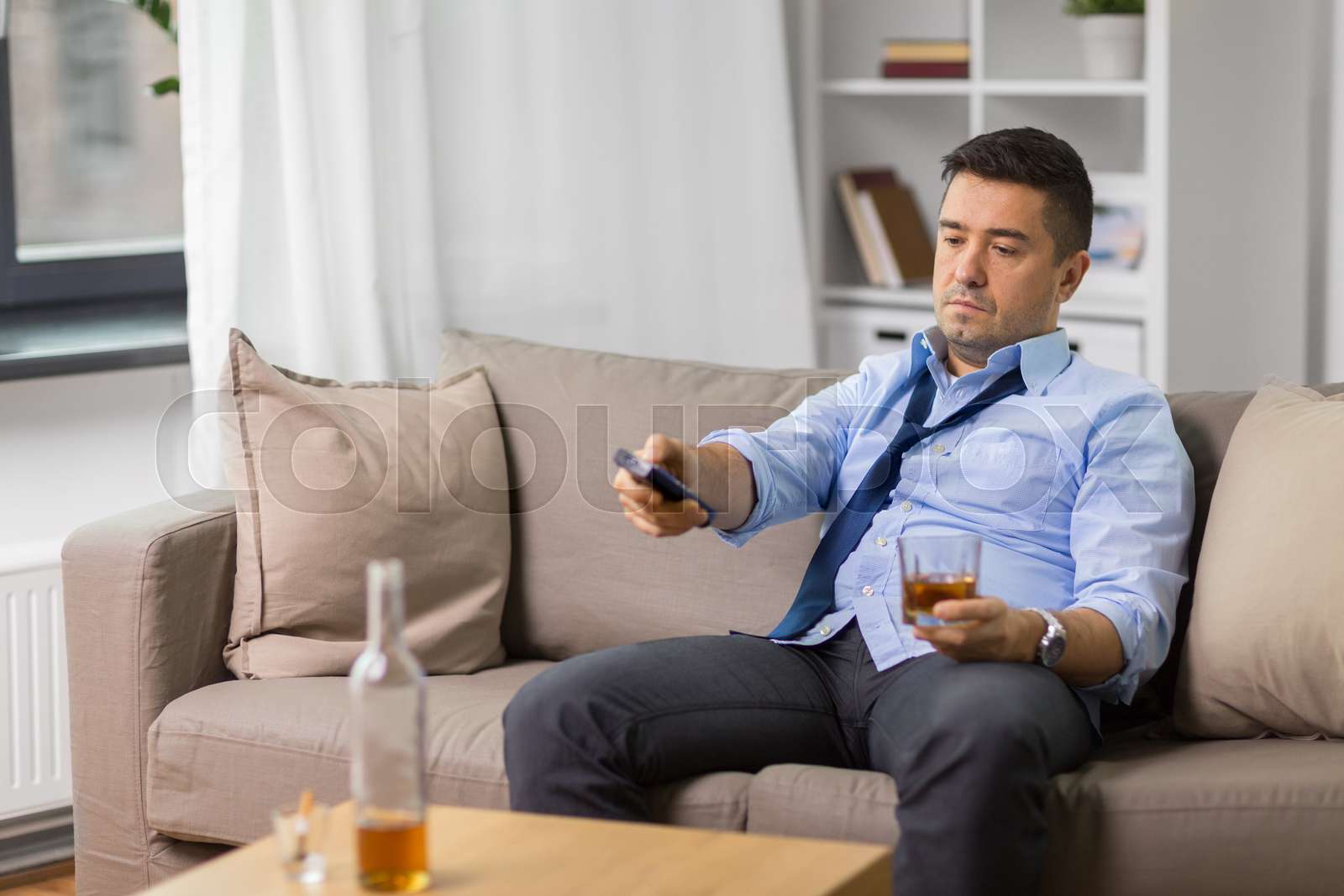 drunk man with tv remote drinking alcohol at home | Stock image | Colourbox