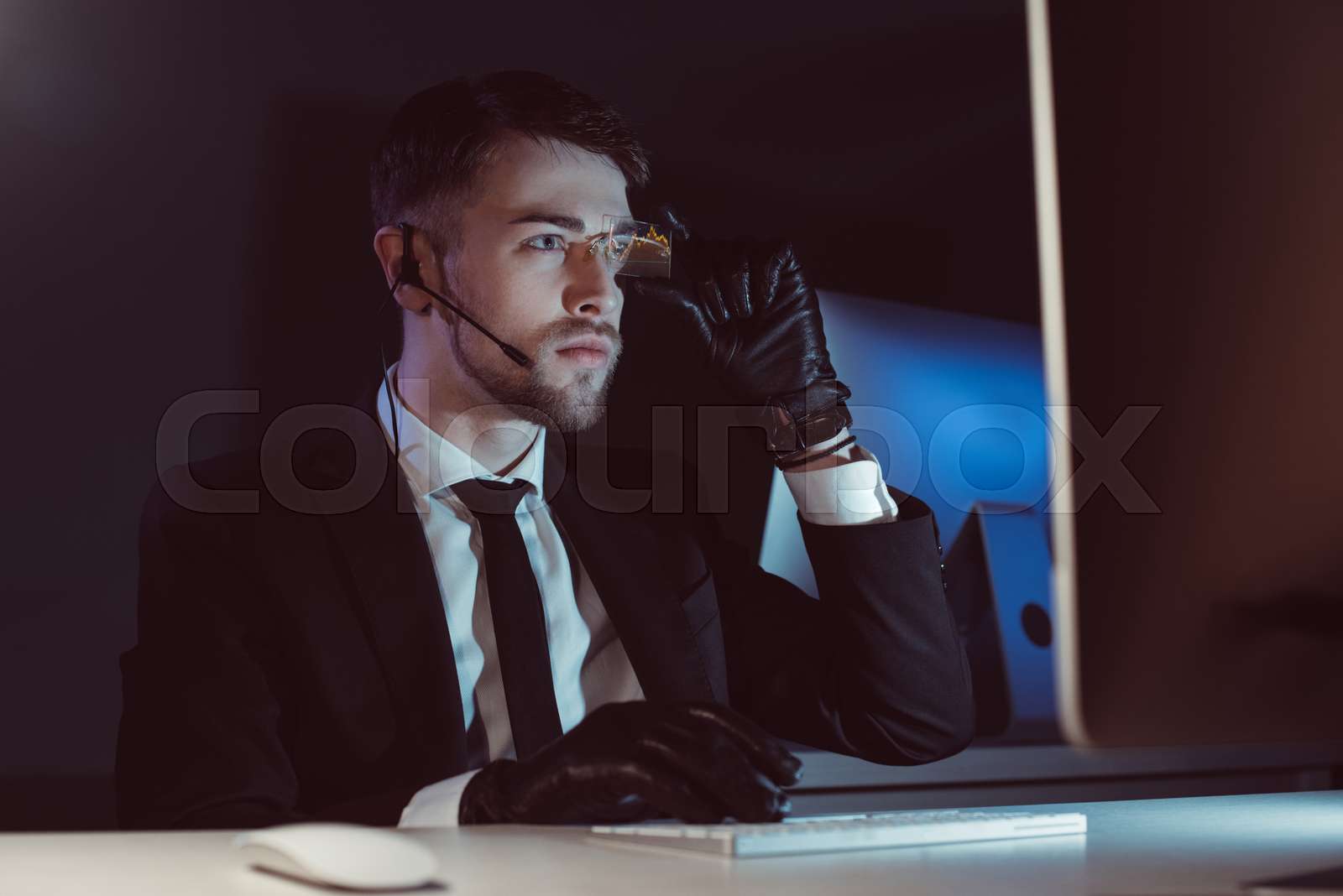 portrait of spy agent with headset looking at computer screen at table ...