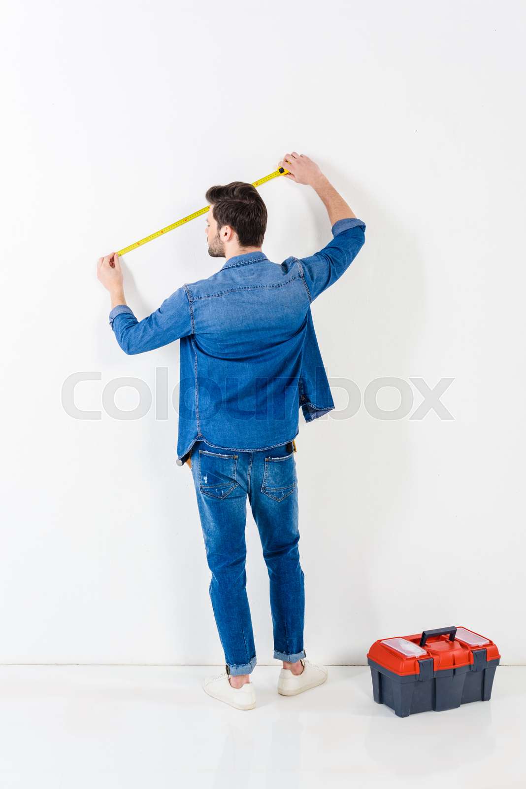 rear view of man measuring wall with tape measure on white | Stock ...