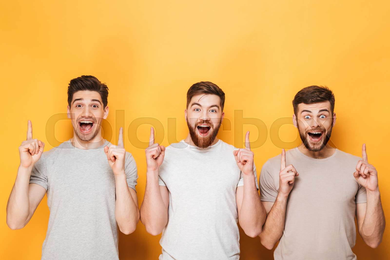 Three young happy men pointing up at copy space | Stock image | Colourbox