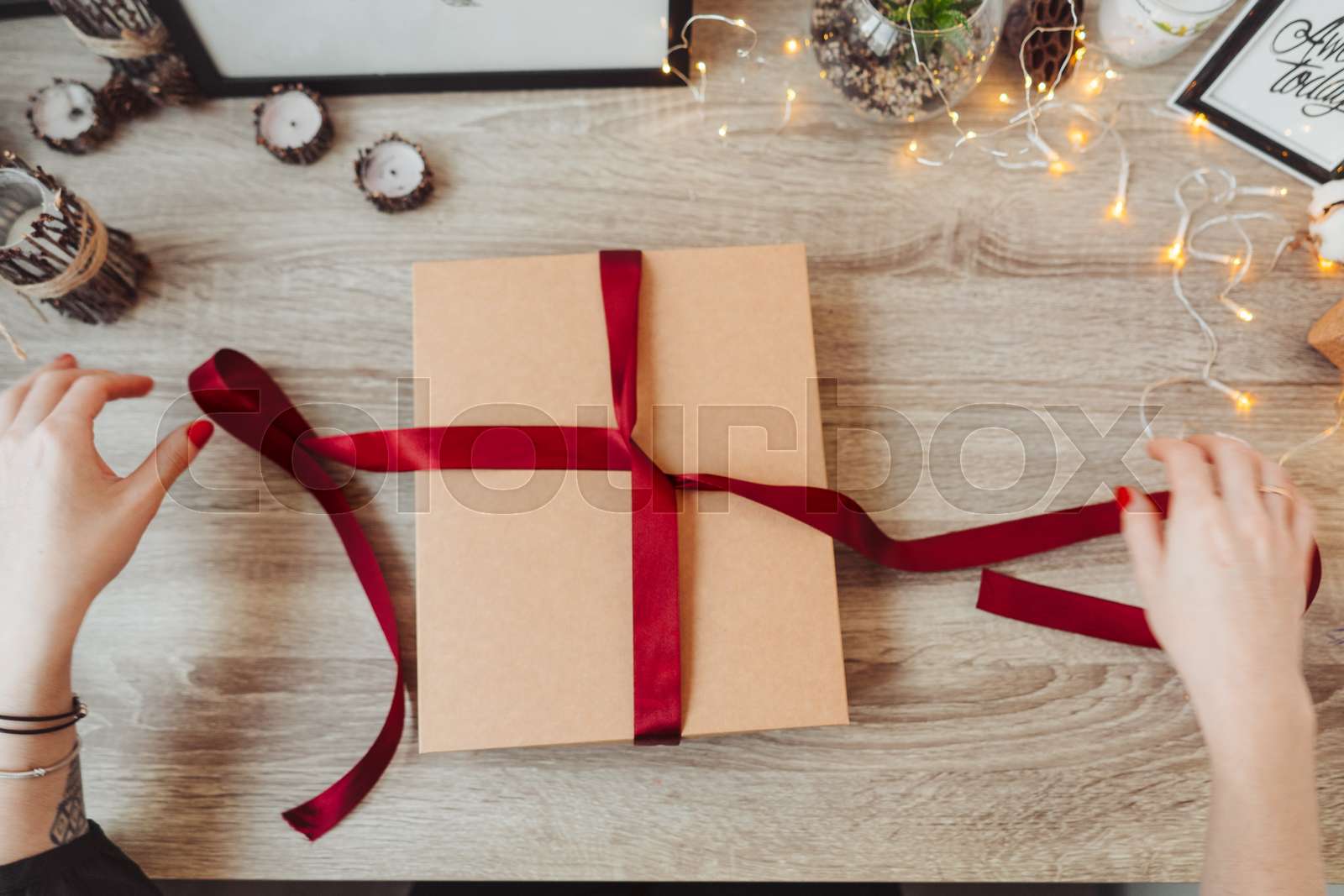 Woman wrapping present in paper with red ribbon. | Stock image | Colourbox