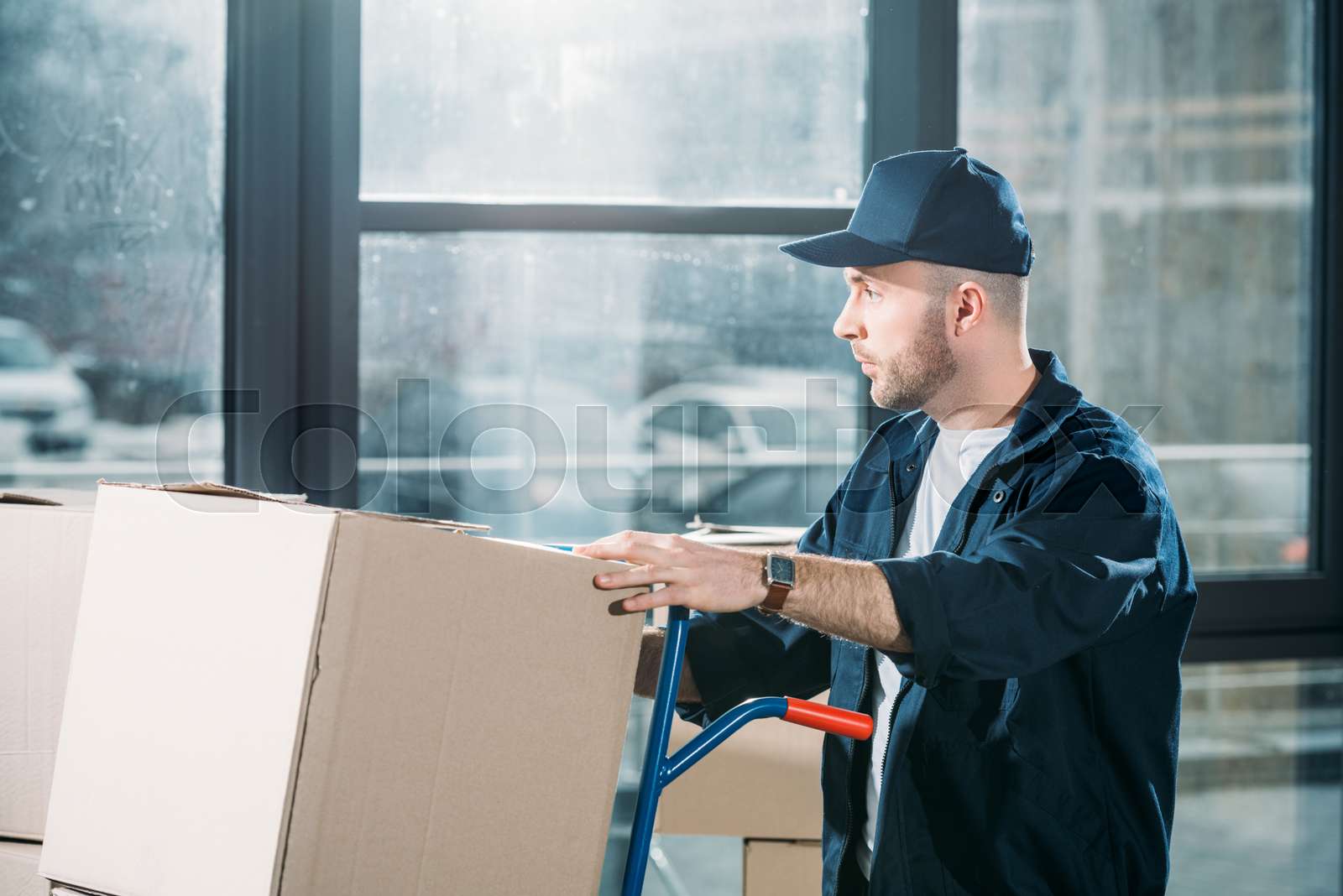Loader man adjusting cardboard boxes on cart | Stock image | Colourbox