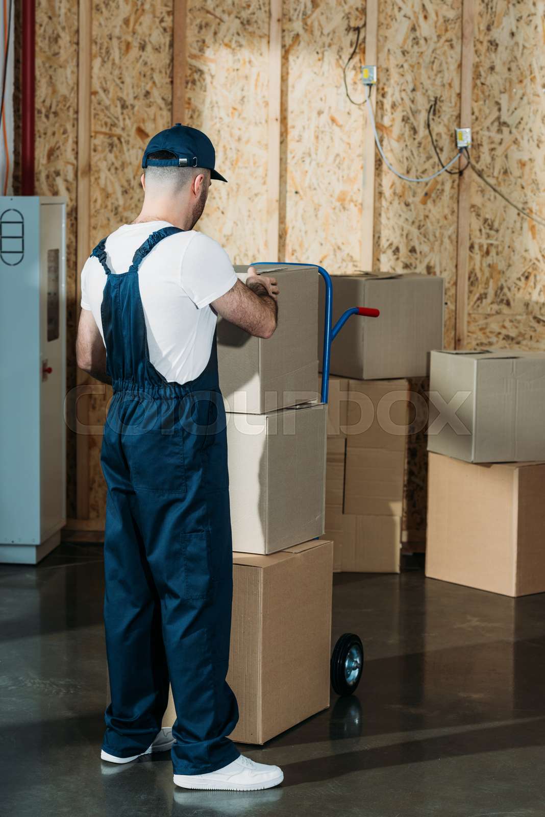 Loader man adjusting cardboard boxes on cart | Stock image | Colourbox