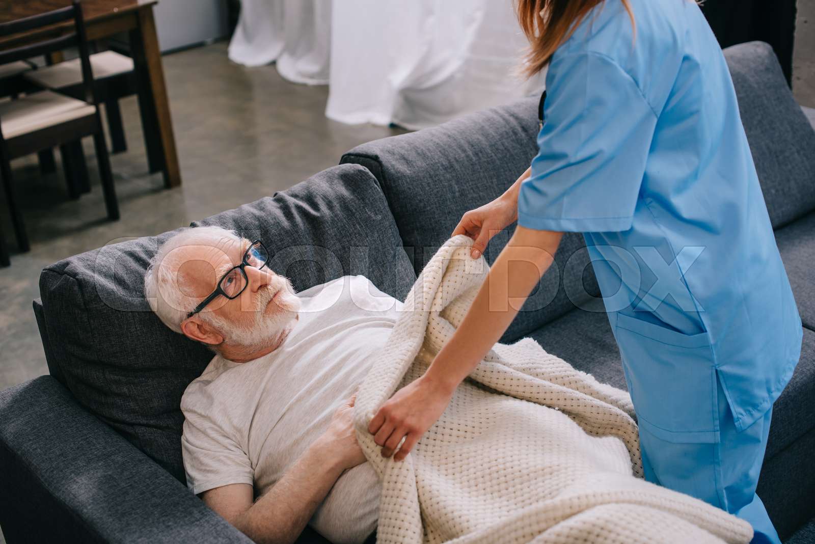 Nurse helping old patient to cover with plaid | Stock image | Colourbox