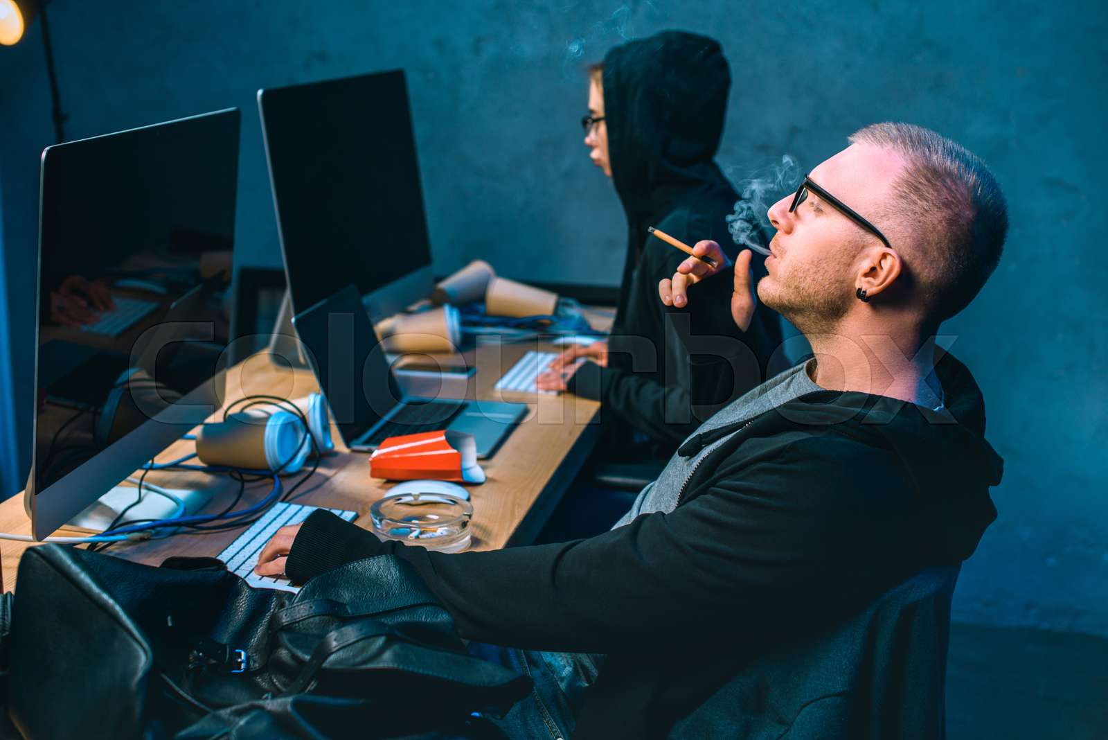 male hacker working on malware with accomplice and smoking | Stock ...