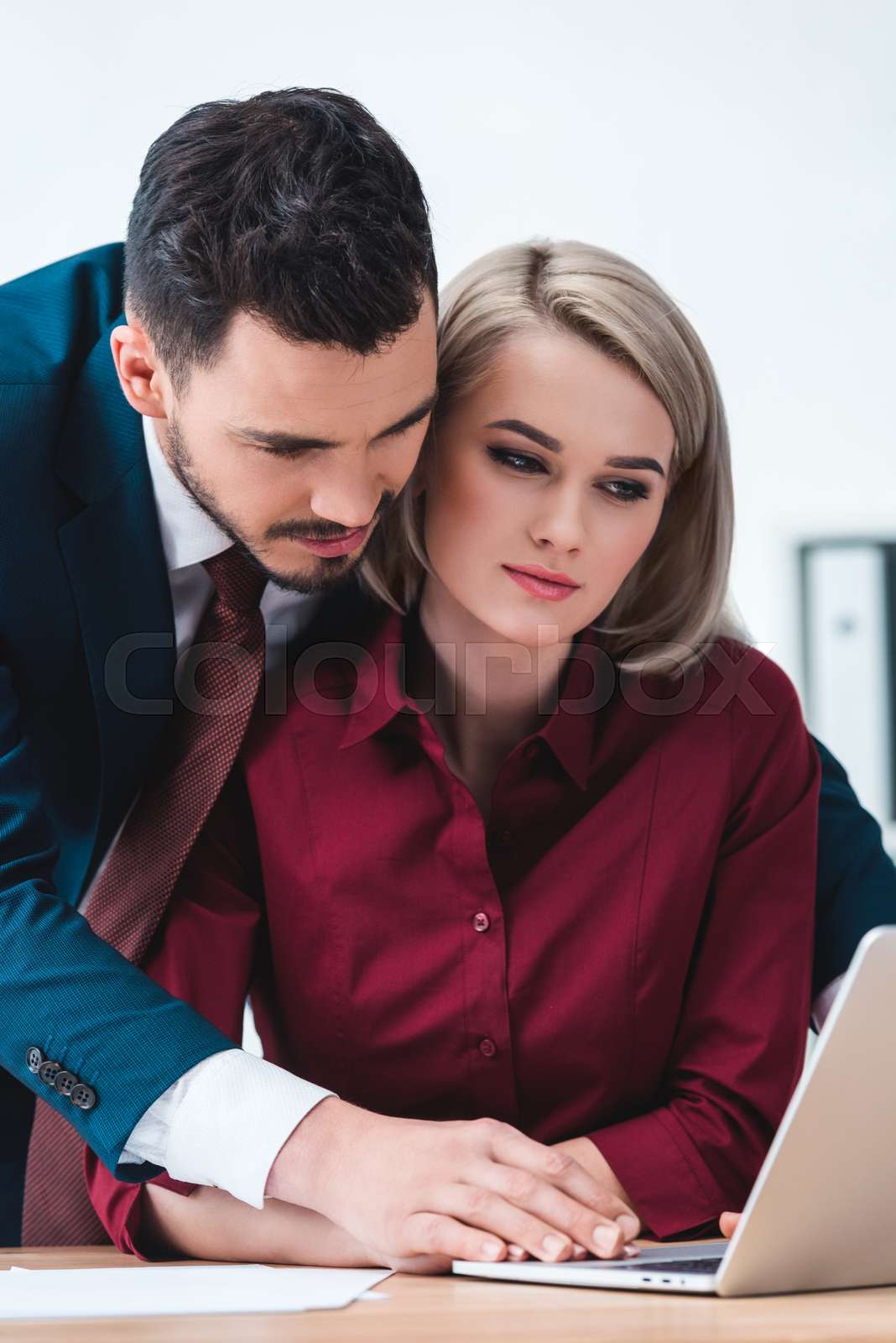 Handsome Businessman Flirting With Beautiful Female Colleague Using Laptop In Office Stock