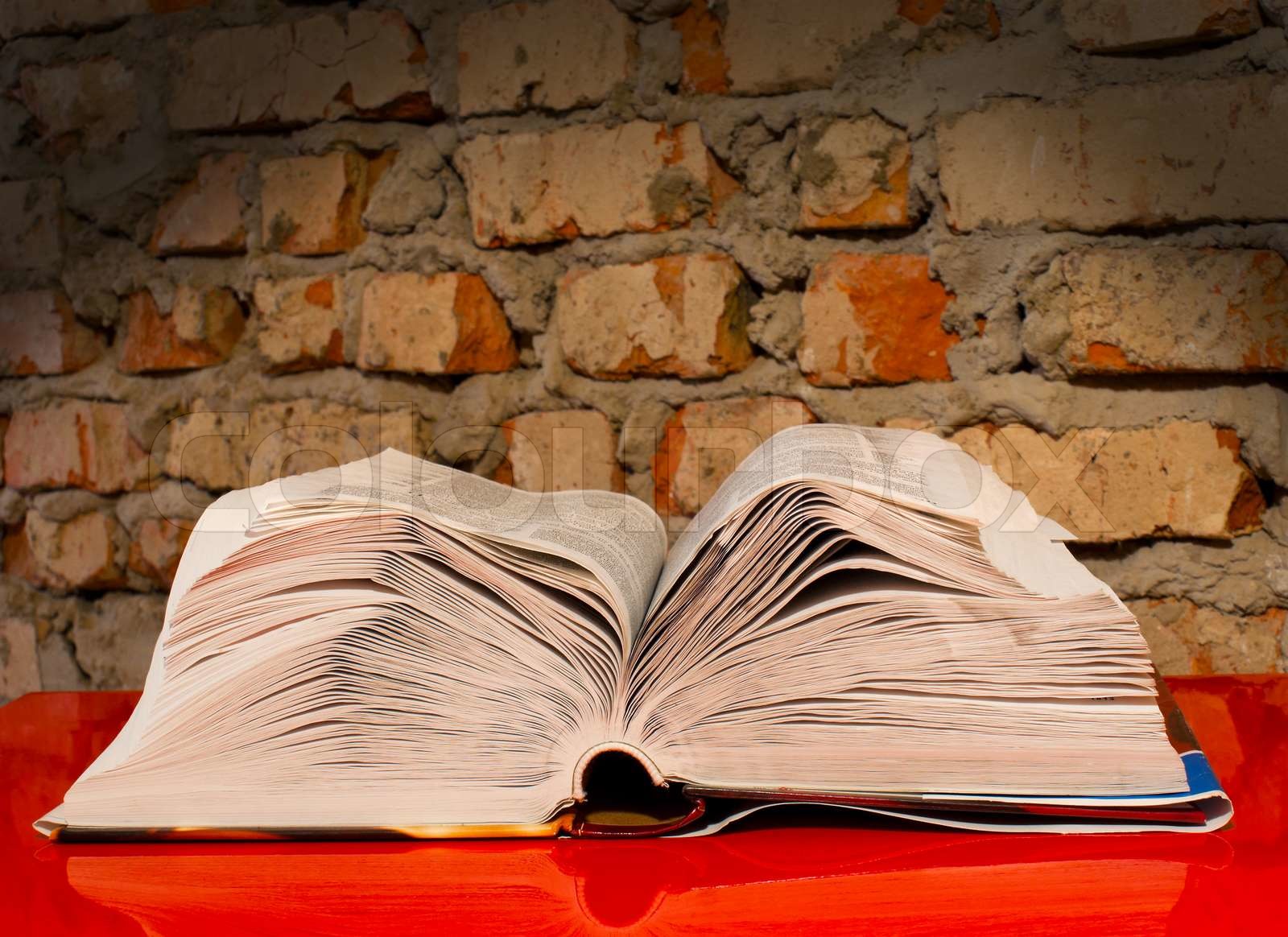 Open book laying on the table against brick wall | Stock image | Colourbox