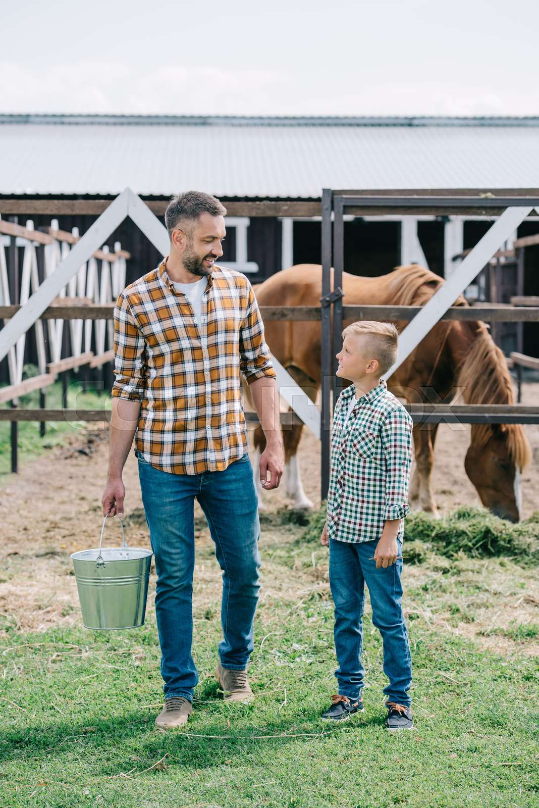 father with bucket and little son smiling each other while standing ...