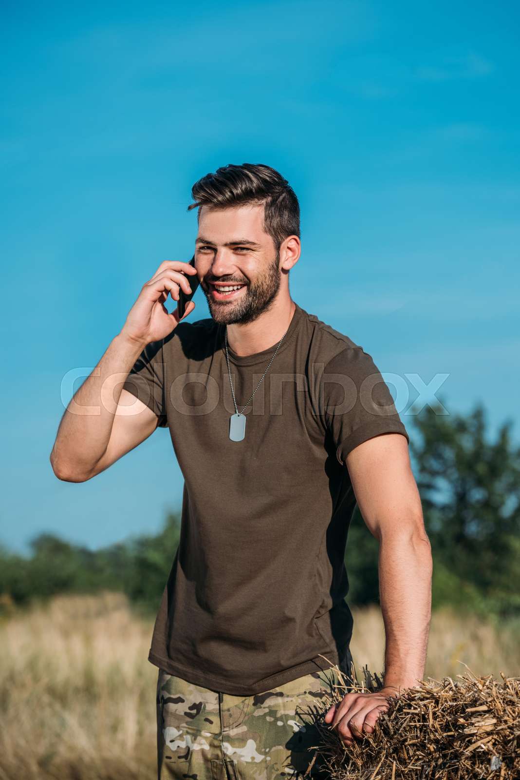smiling soldier in military uniform talking on smartphone on range ...