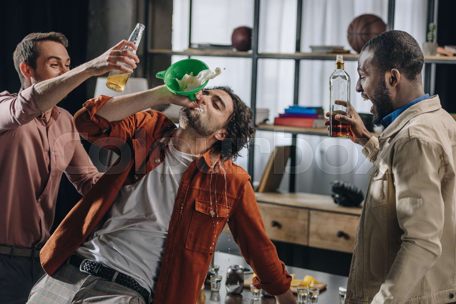 drunk male friends drinking alcohol beverages from funnel at party ...
