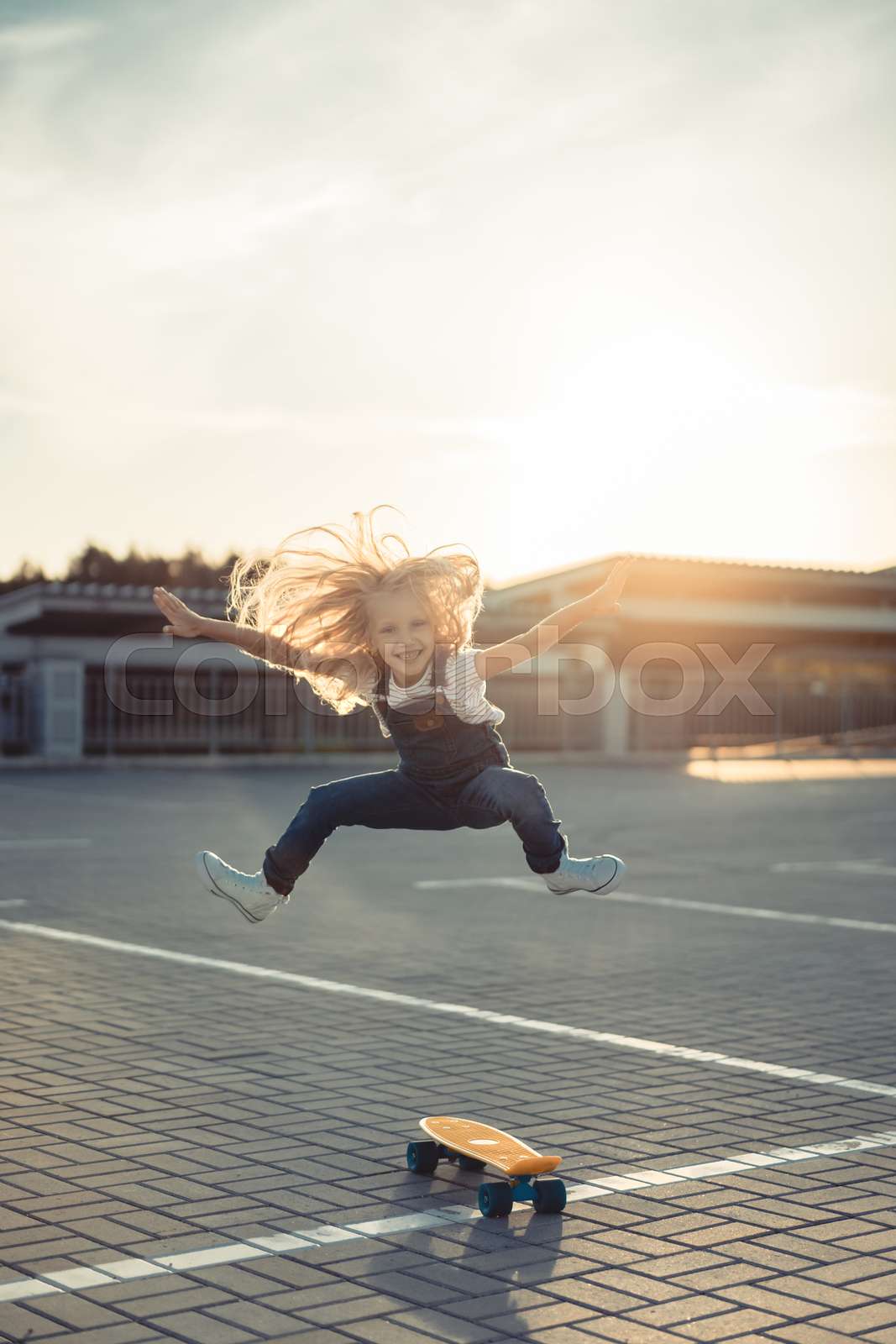 happy little child jumping with wide arms near skateboard at parking ...