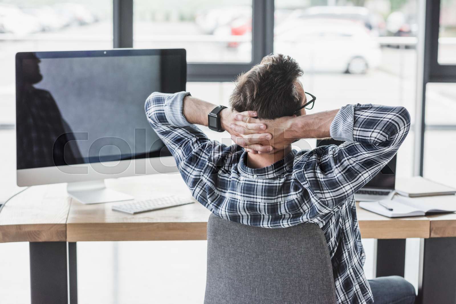 back view of programmer sitting with hands behind head at workplace ...