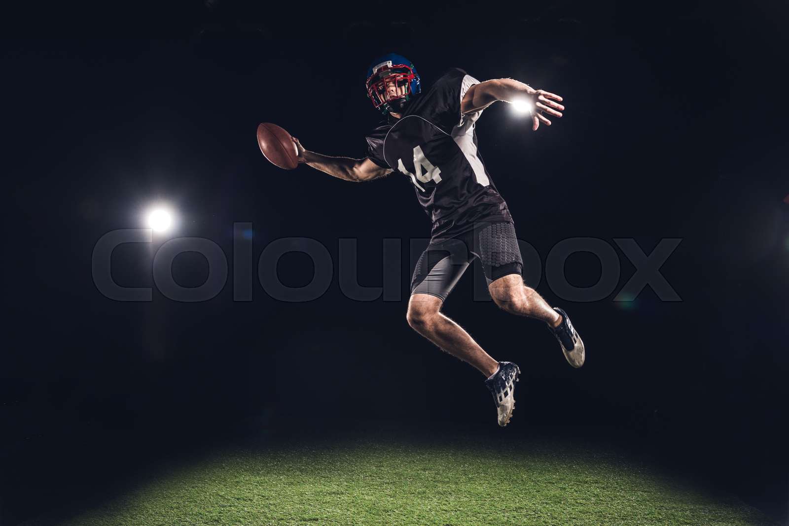 american football player jumping with ball under spotlights on black ...