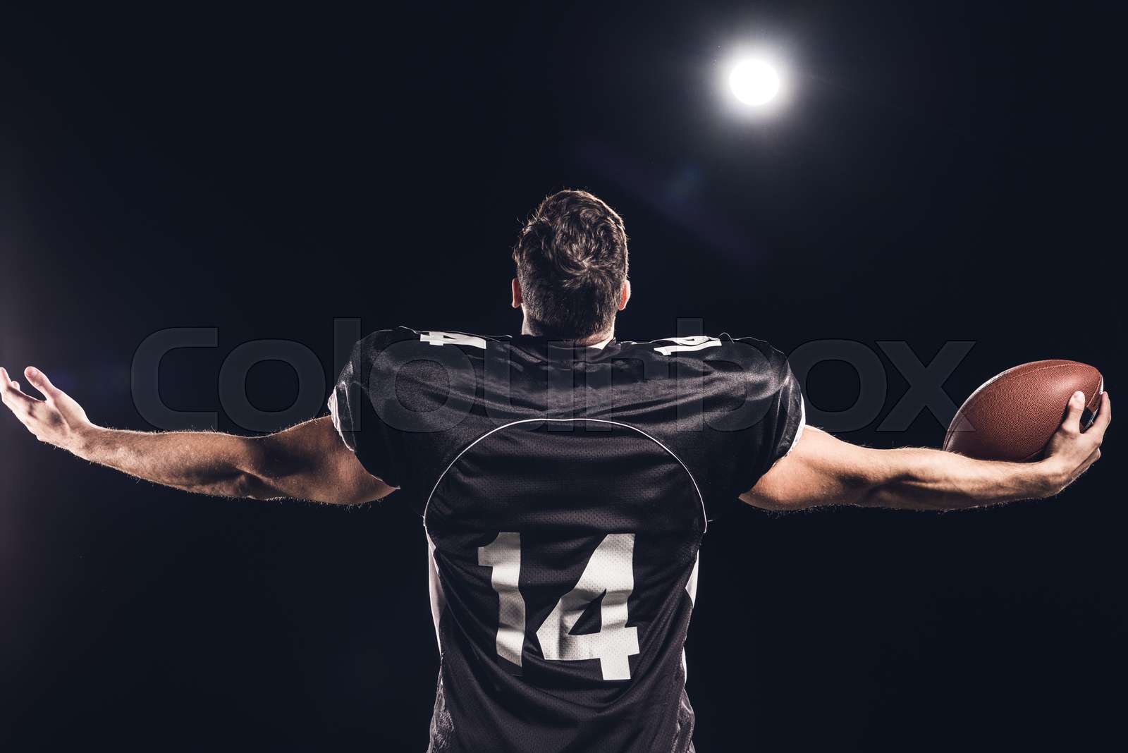 rear view of american football player with ball looking up with ...