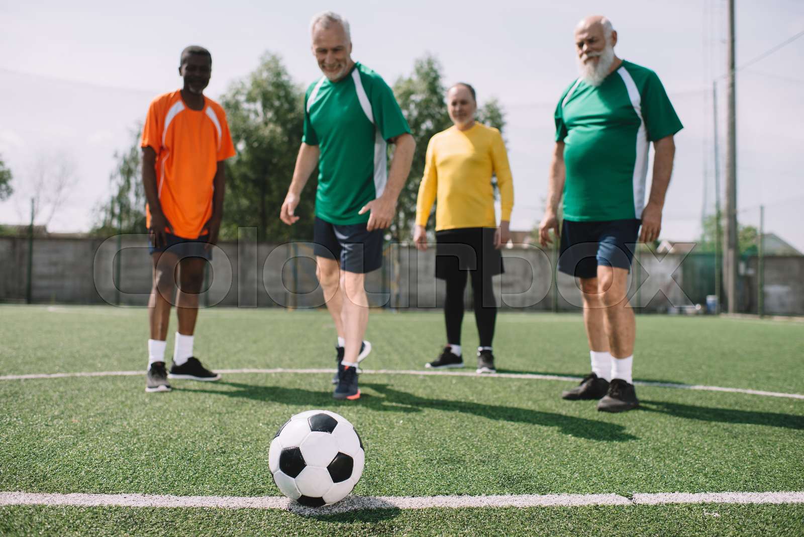 selective focus of football ball and multicultural elderly men on green ...